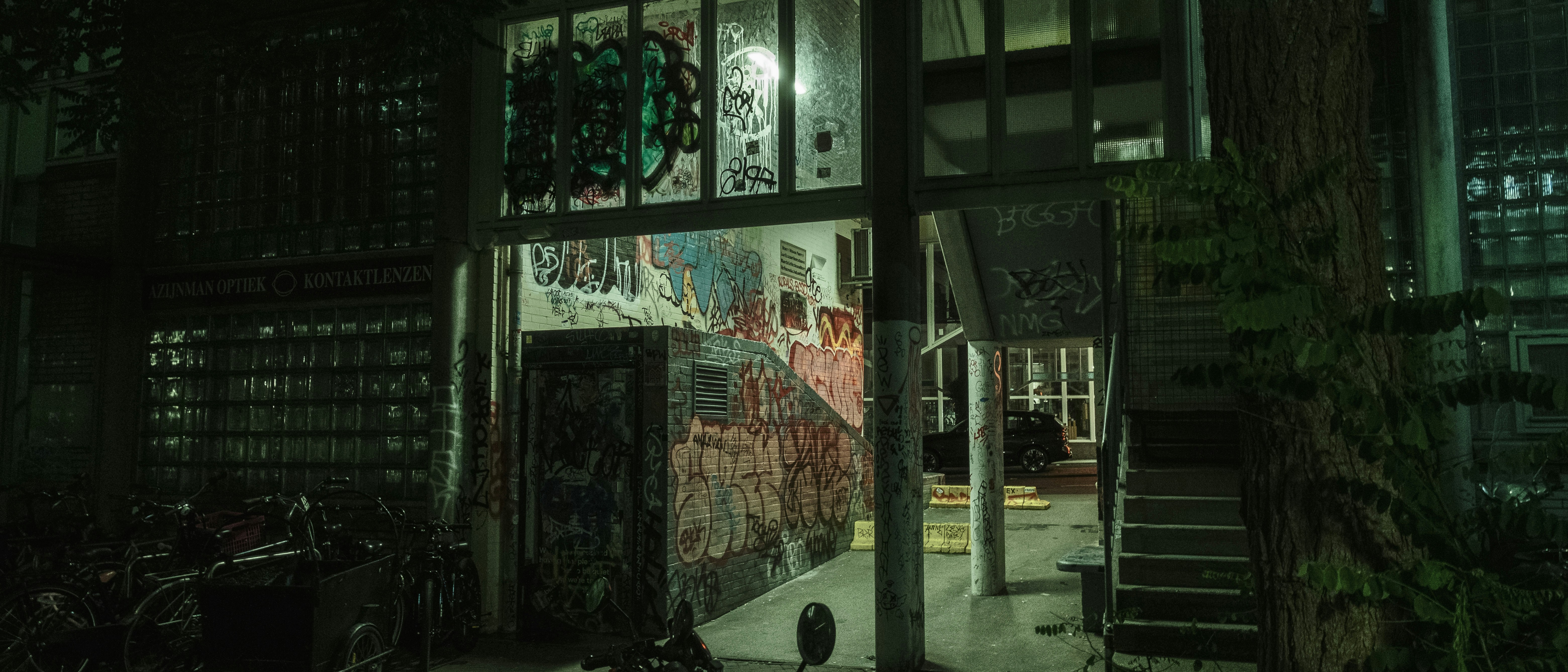 Dimly lit corridor adorned with vibrant graffiti and bicycles, leading to a stairway in an urban setting.