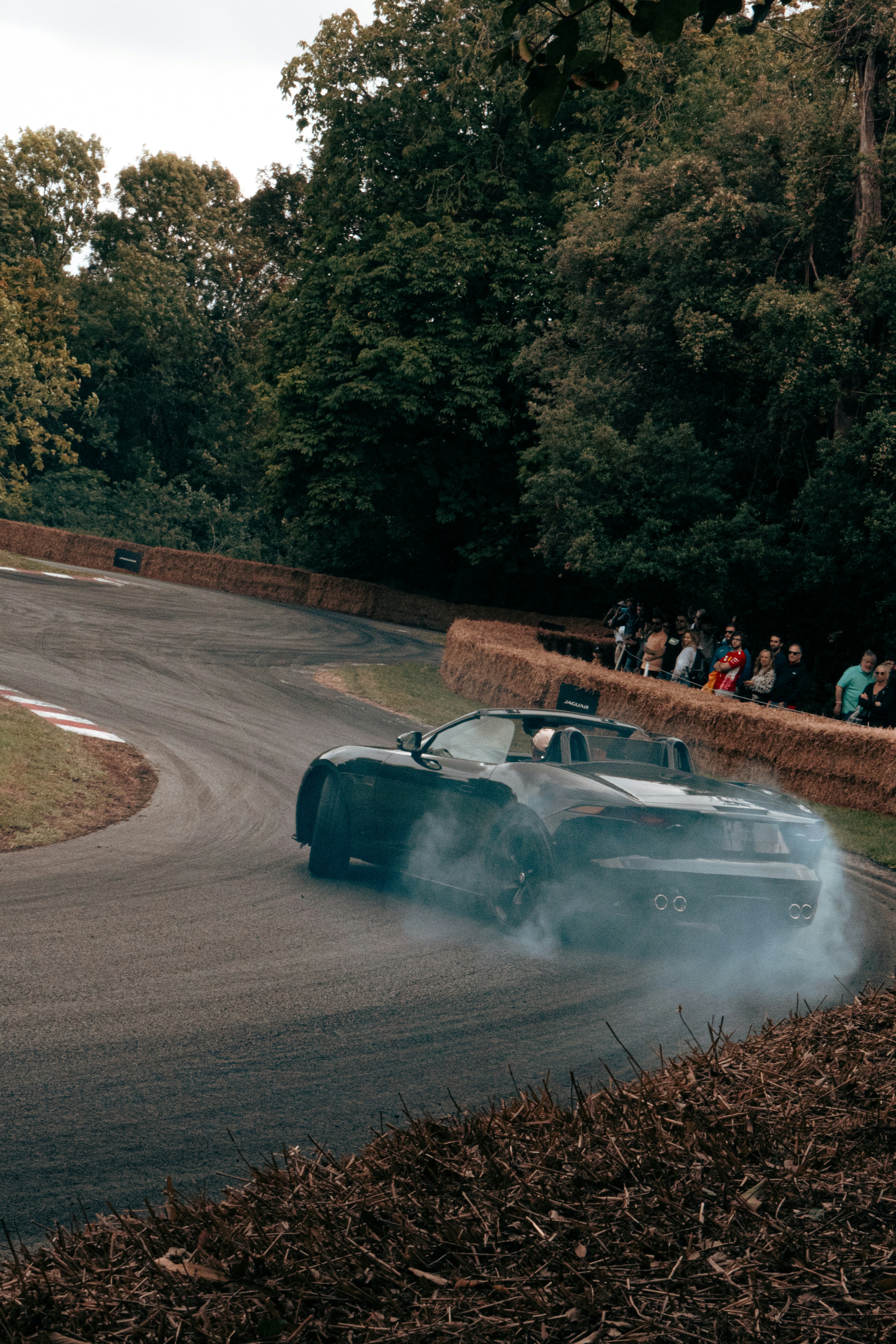 A car drifting at the Goodwood Festival of Speed 2023 | A dark car drifts around a corner, creating smoke.