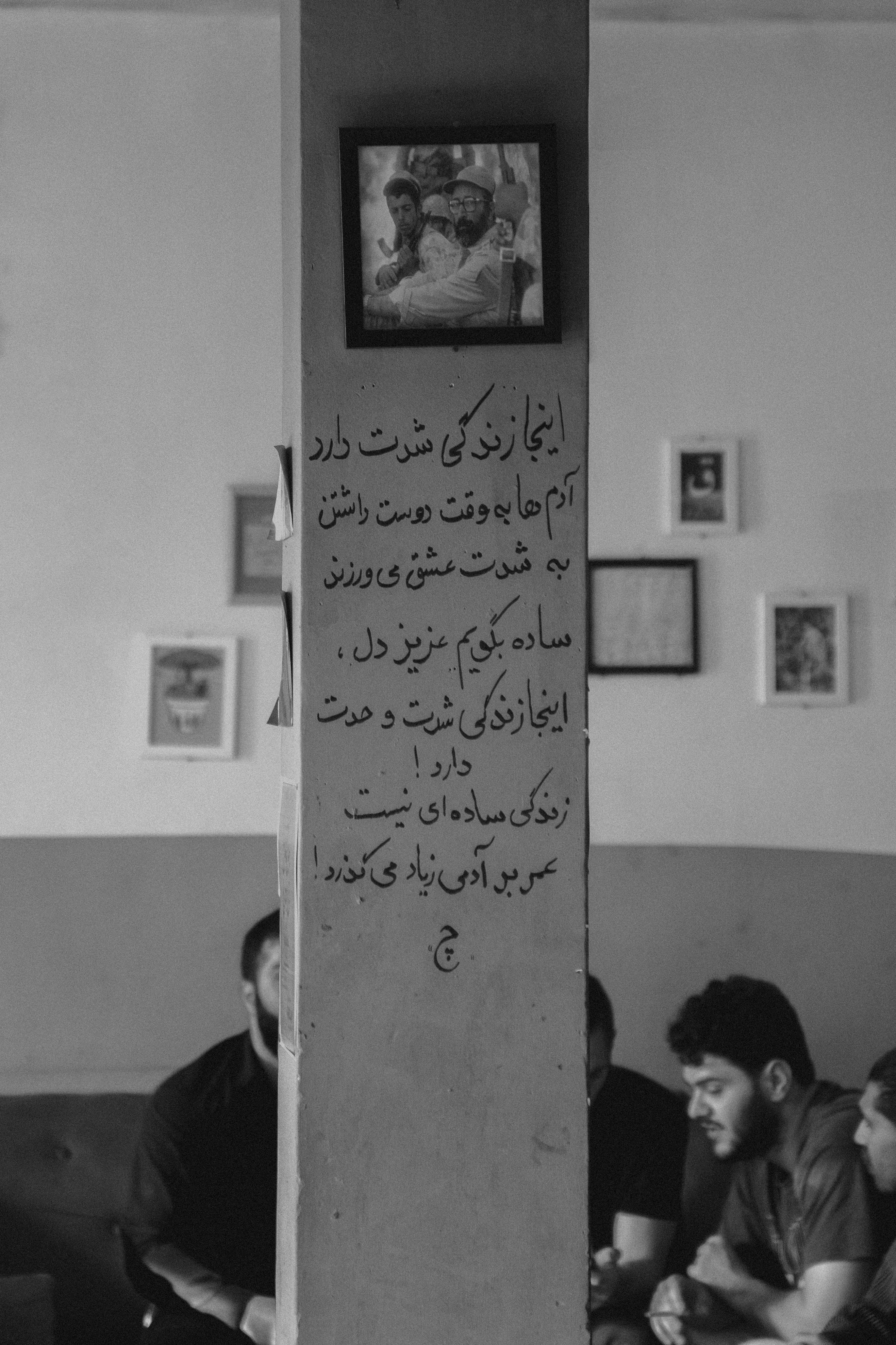 People sitting in a room with writing on a pillar.