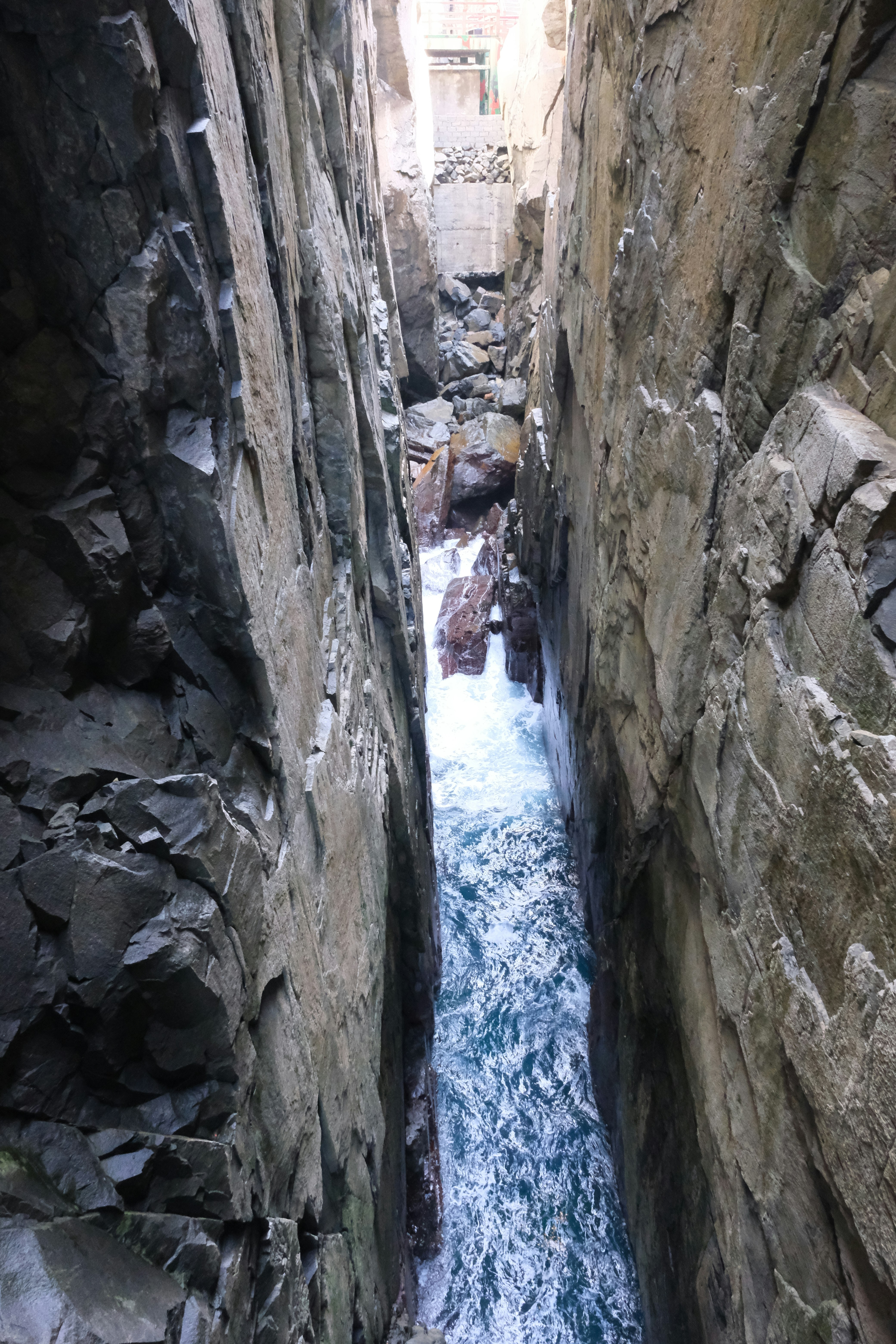 Rushing water flows through a narrow canyon surrounded by towering rock walls, showcasing the power of nature's erosion. The scene captures the dynamic interplay between water and stone.