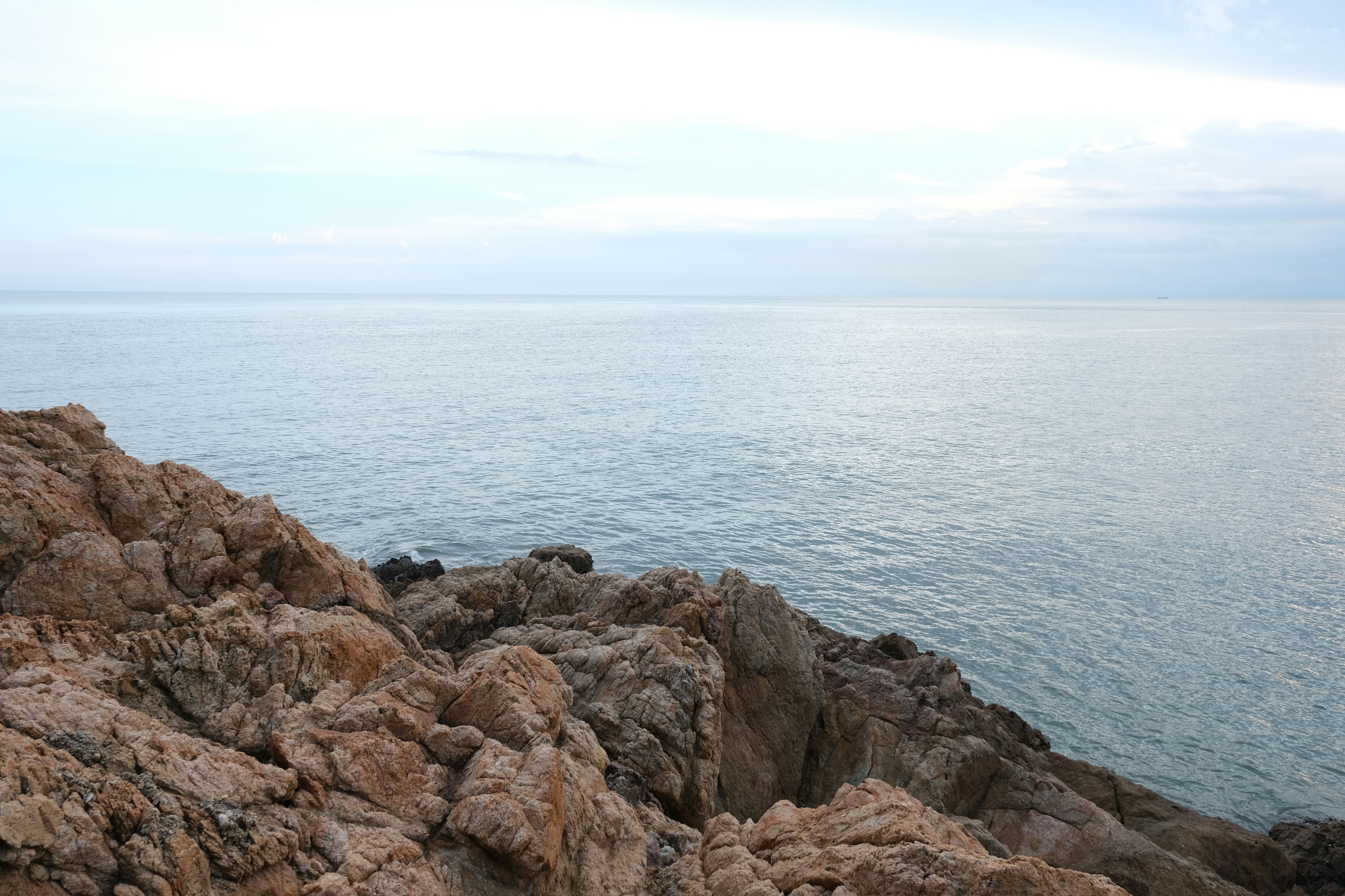 Rocky coastline meets the calm ocean under a hazy sky