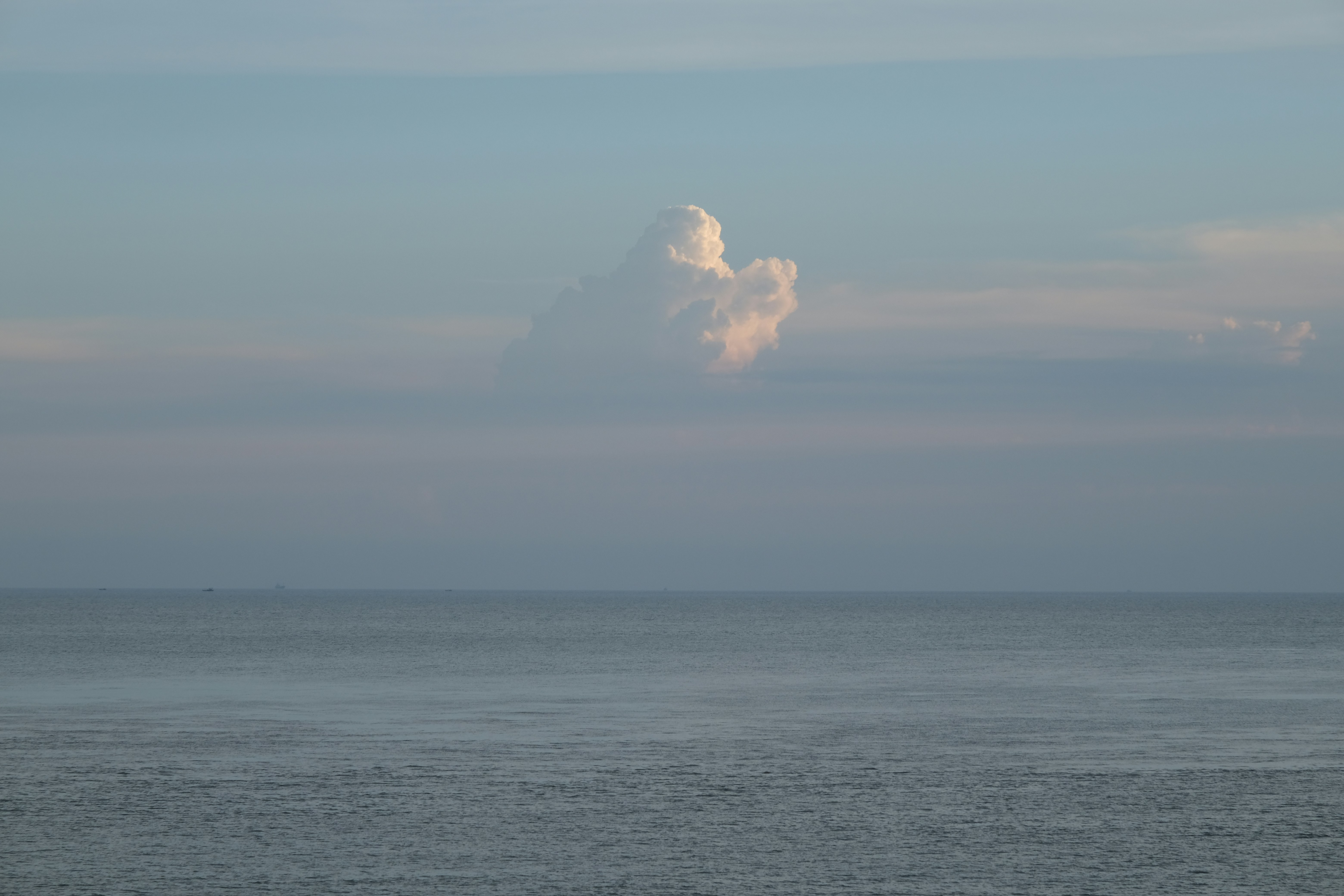 A single cloud floats over a calm ocean.