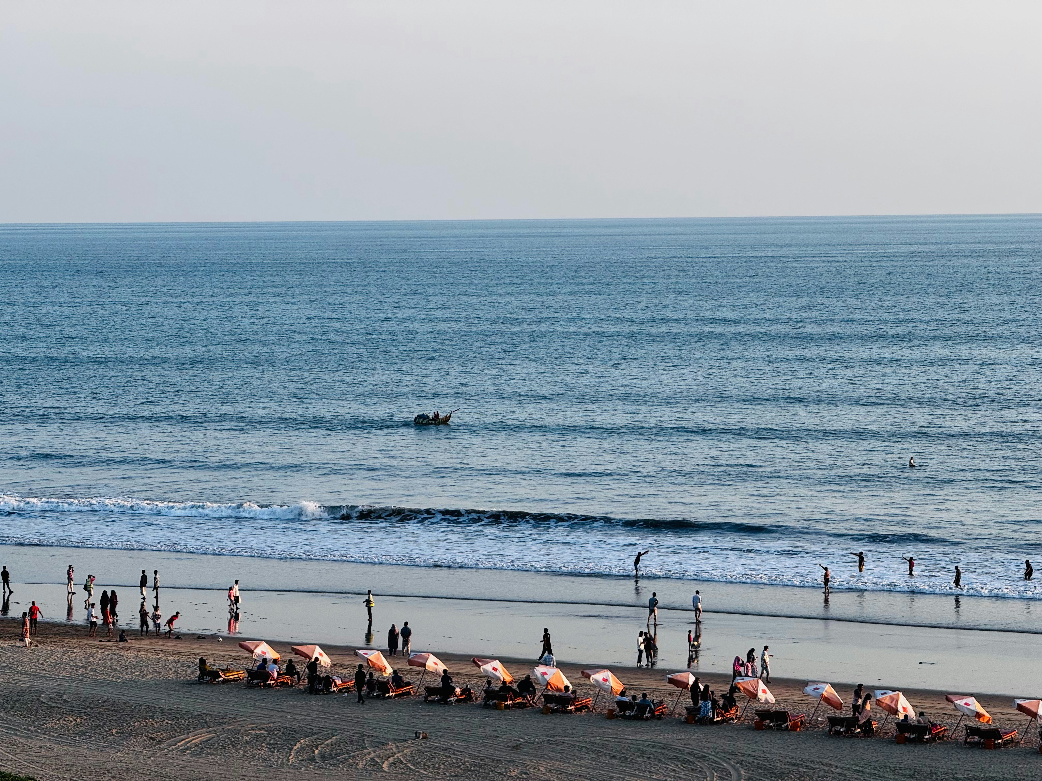 Beachgoers enjoying a sunny day along the shoreline, with colorful umbrellas lining the sand and gentle waves lapping at the shore.