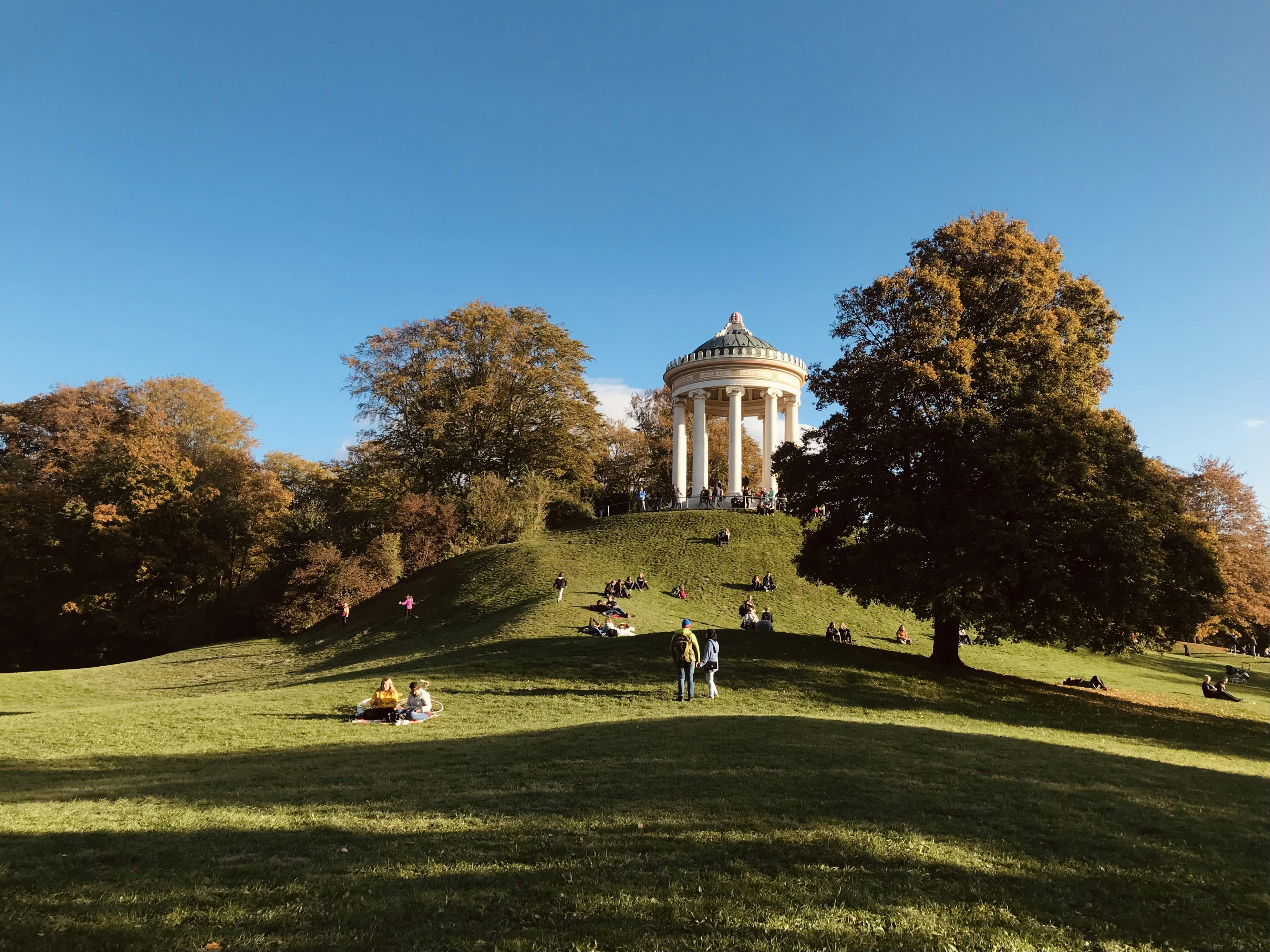People relaxing on a grassy hill near a domed building.