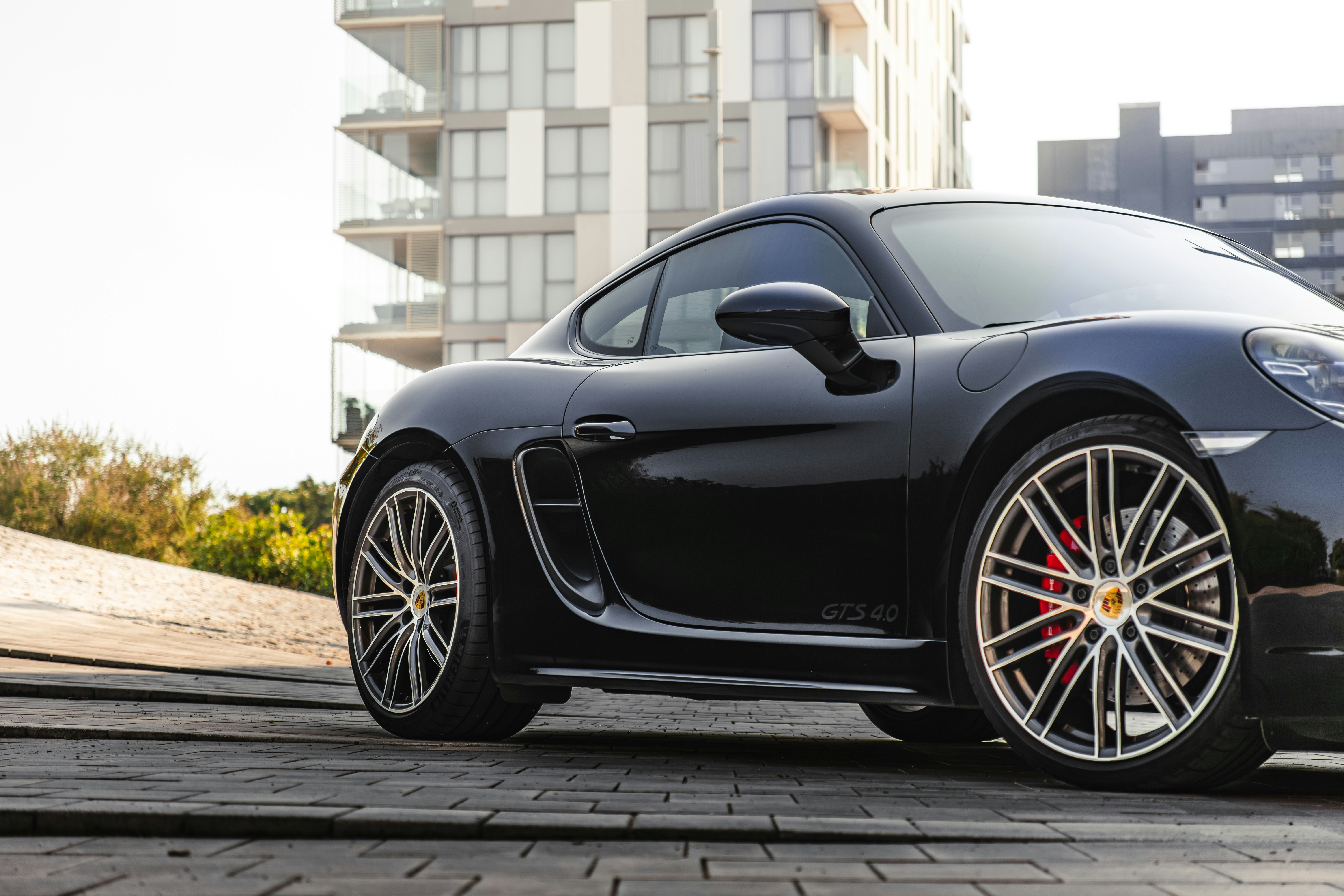 Black Porsche GTS 4.0 parked on a modern urban pathway, showcasing its sleek design and intricate wheel details.