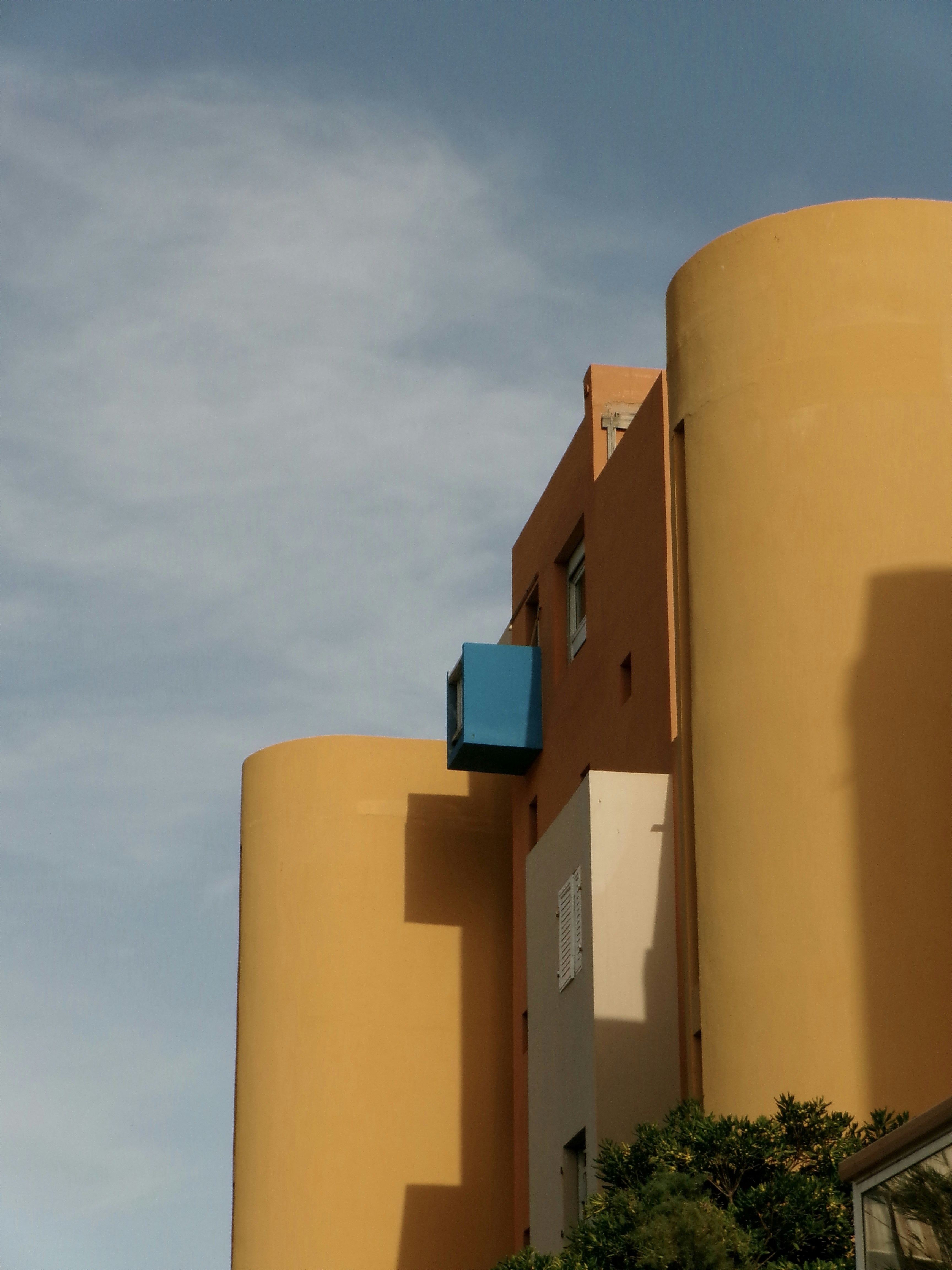 A striking modern building featuring bold cylindrical shapes and a vibrant blue balcony. The interplay of colors and shadows adds depth to the architectural design.