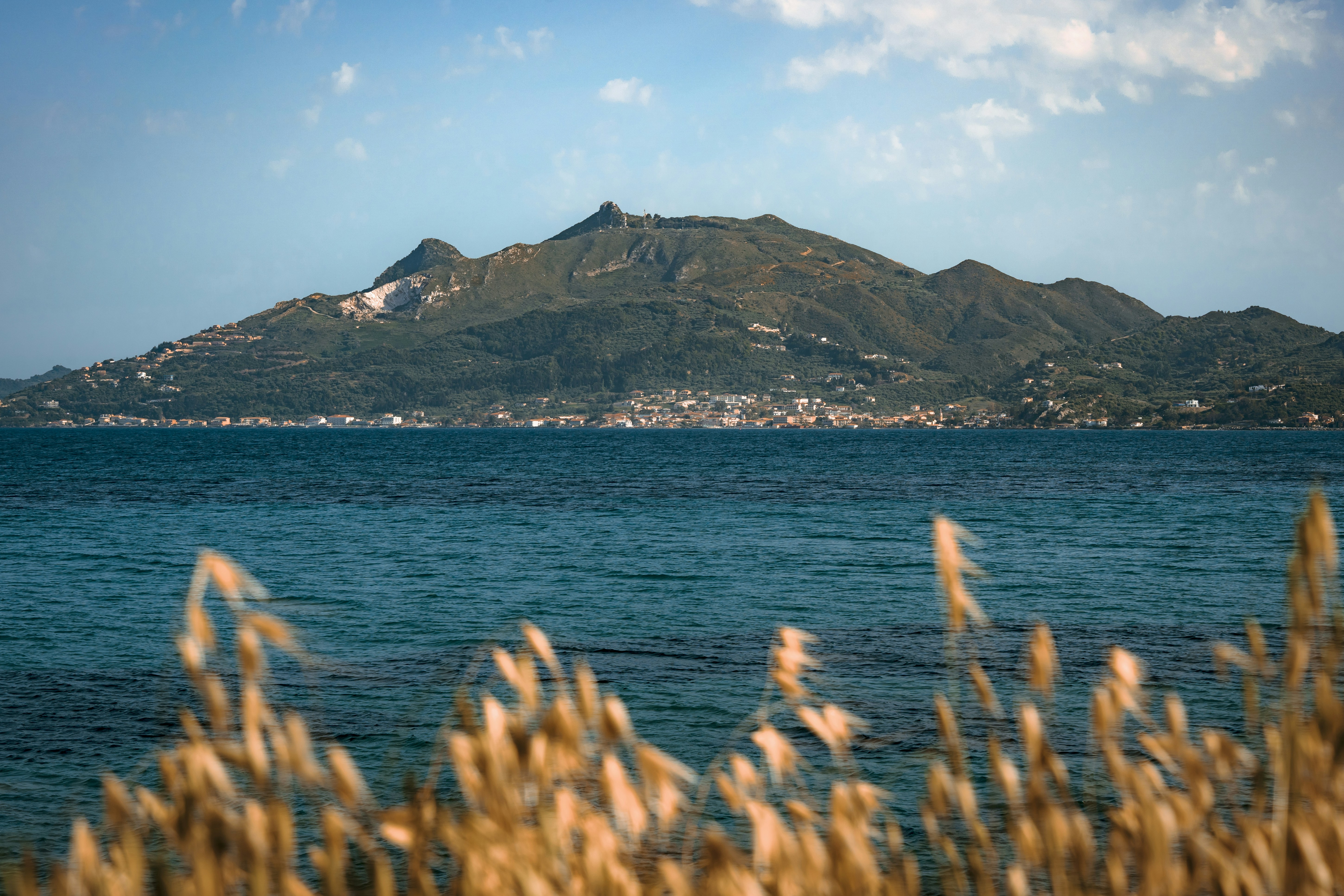 Green mountain range overlooking blue ocean with dry grass