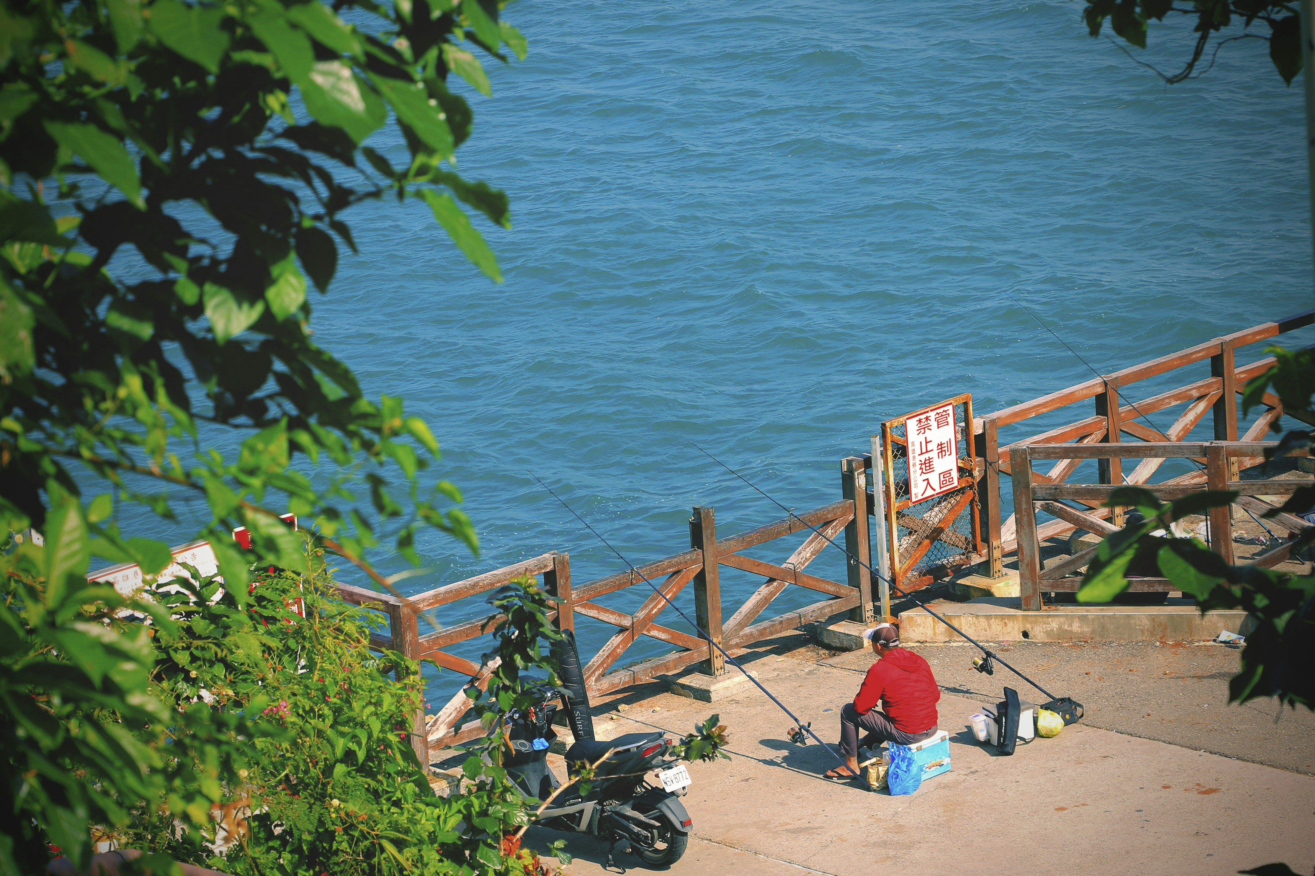 Man fishing by the blue ocean from a wooden pier.
