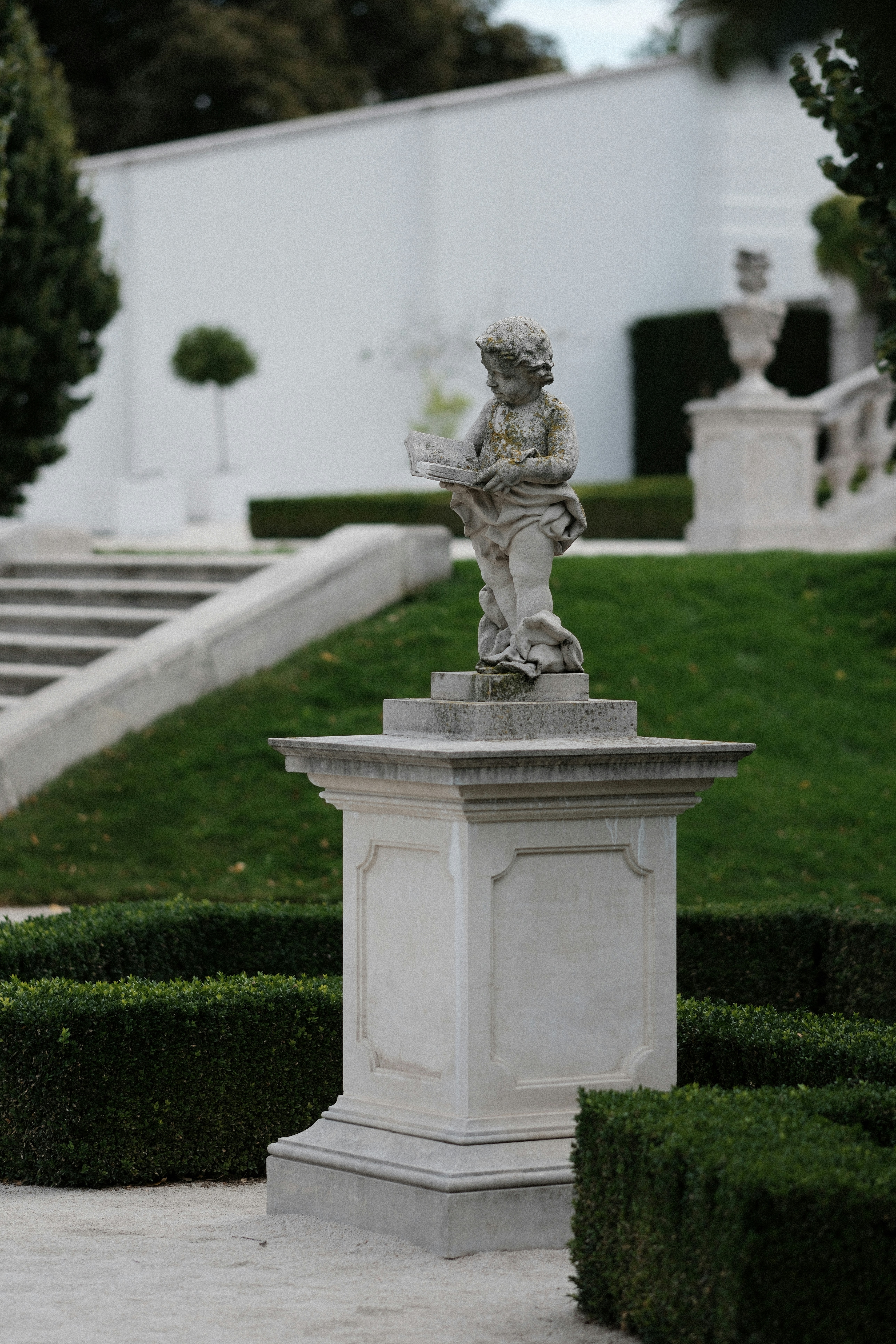 The Reader in White Marble: A Child Statue Amid Precise Garden Geometry