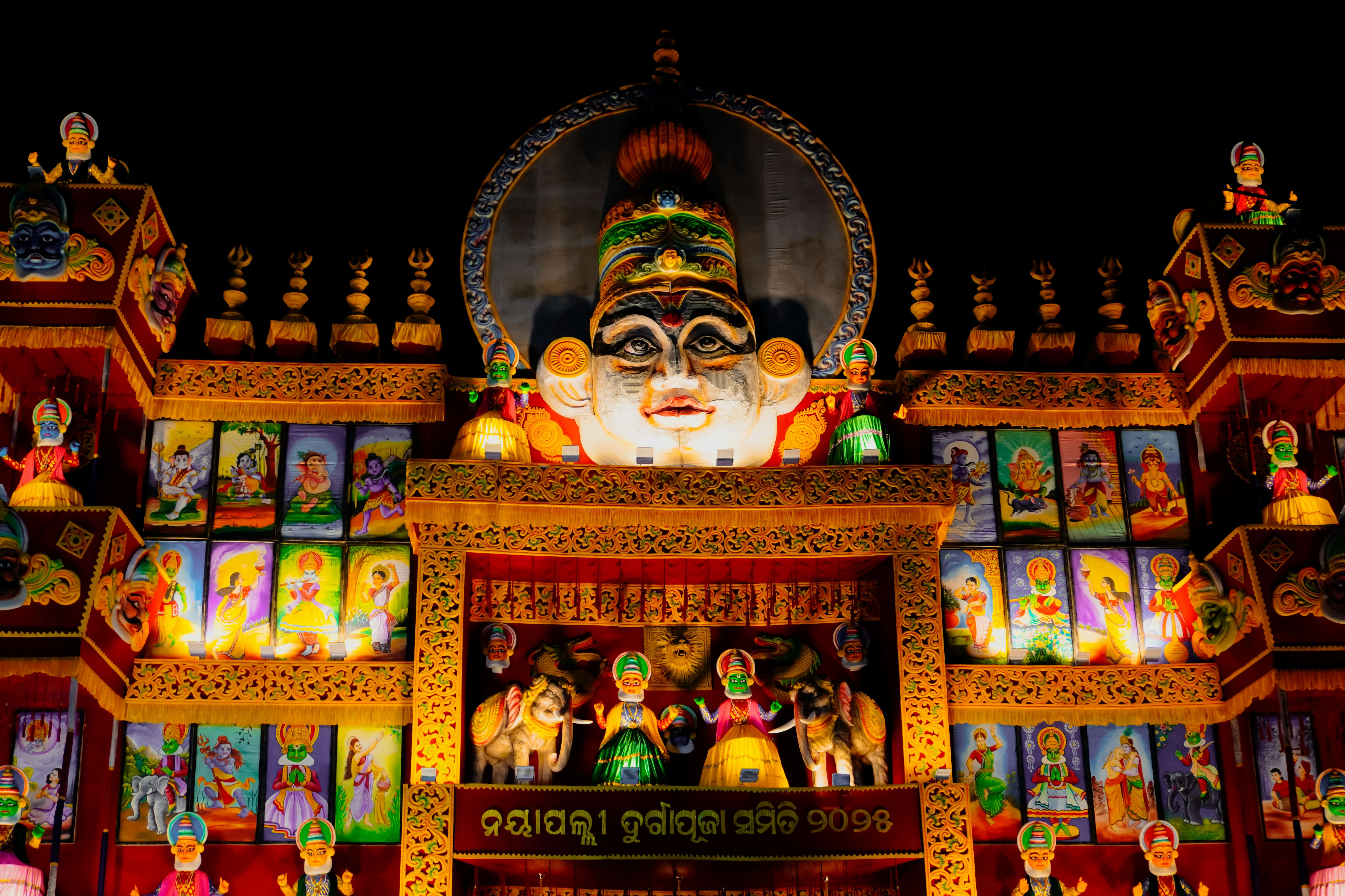 Gilded Guardian: Central Deity Framed by a Tapestry of Deities at Night