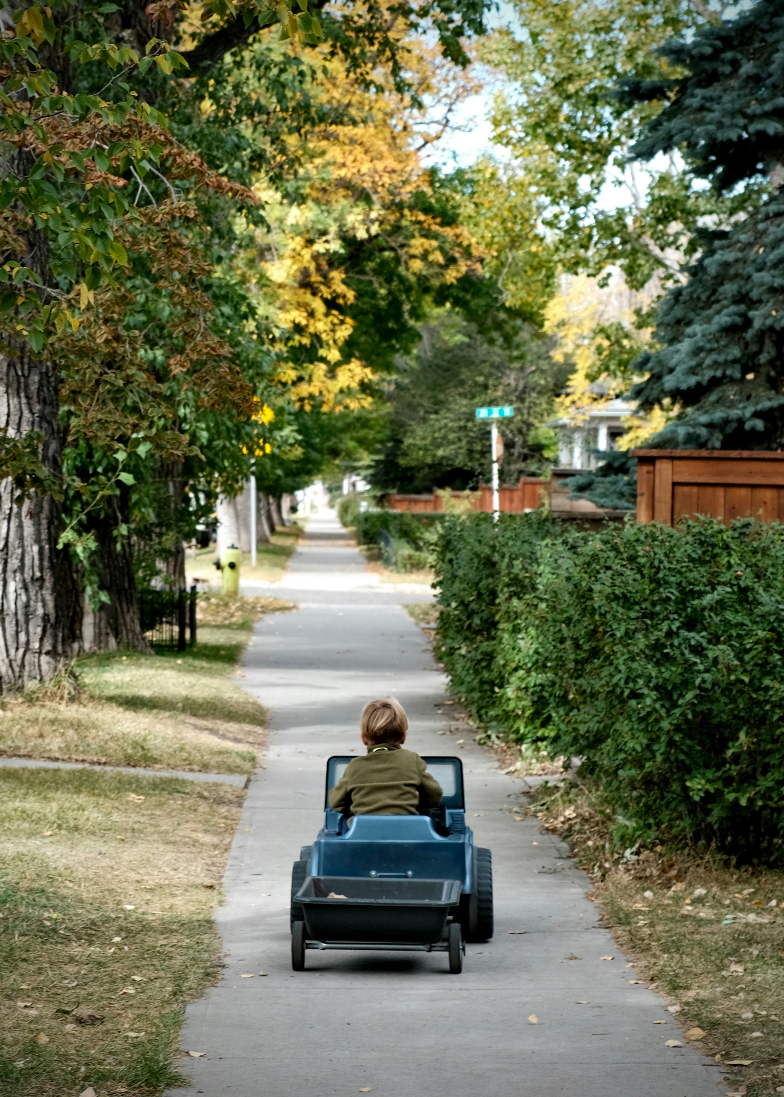 Child rides toy car down suburban sidewalk
