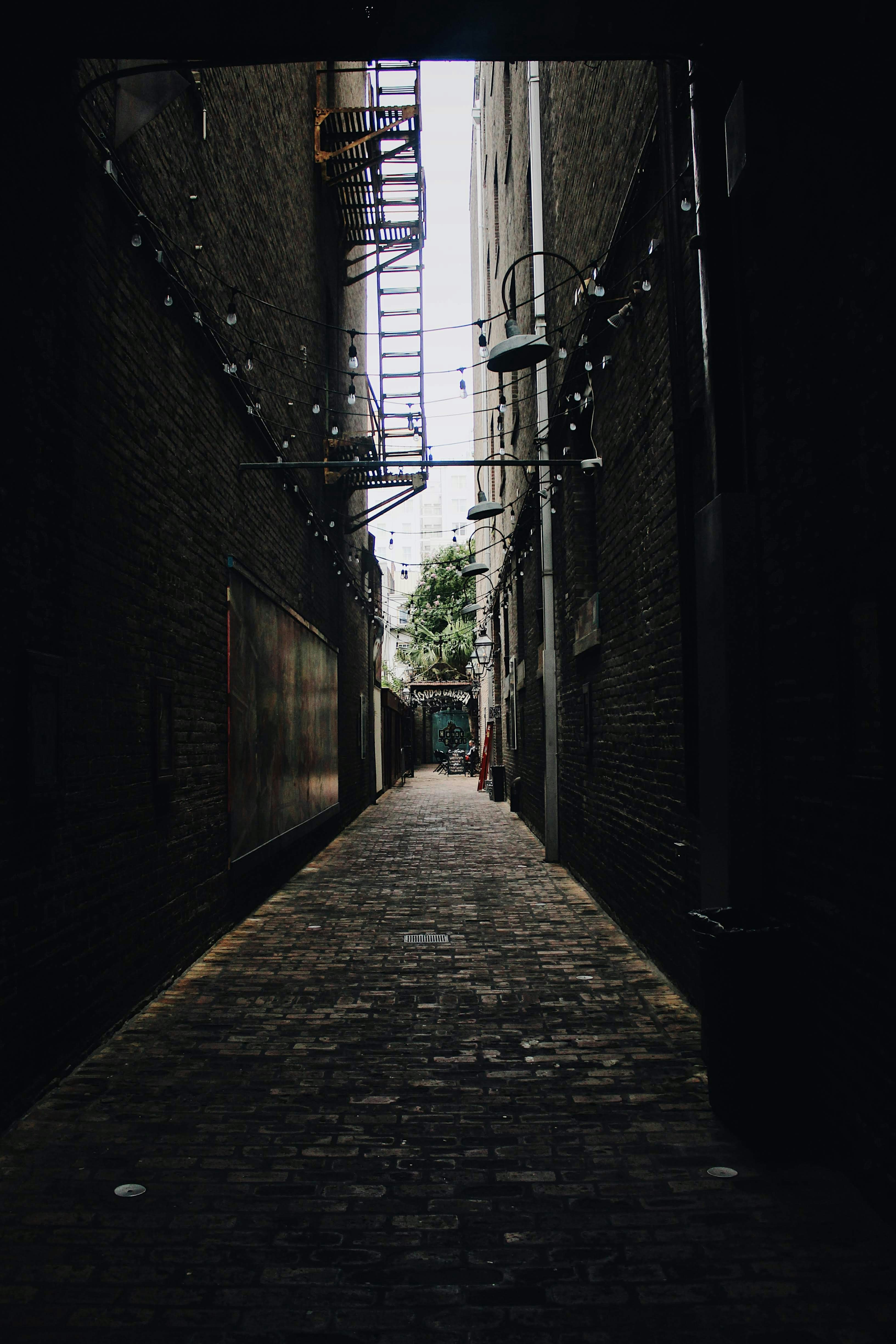 Narrow brick alleyway with string lights and fire escape.