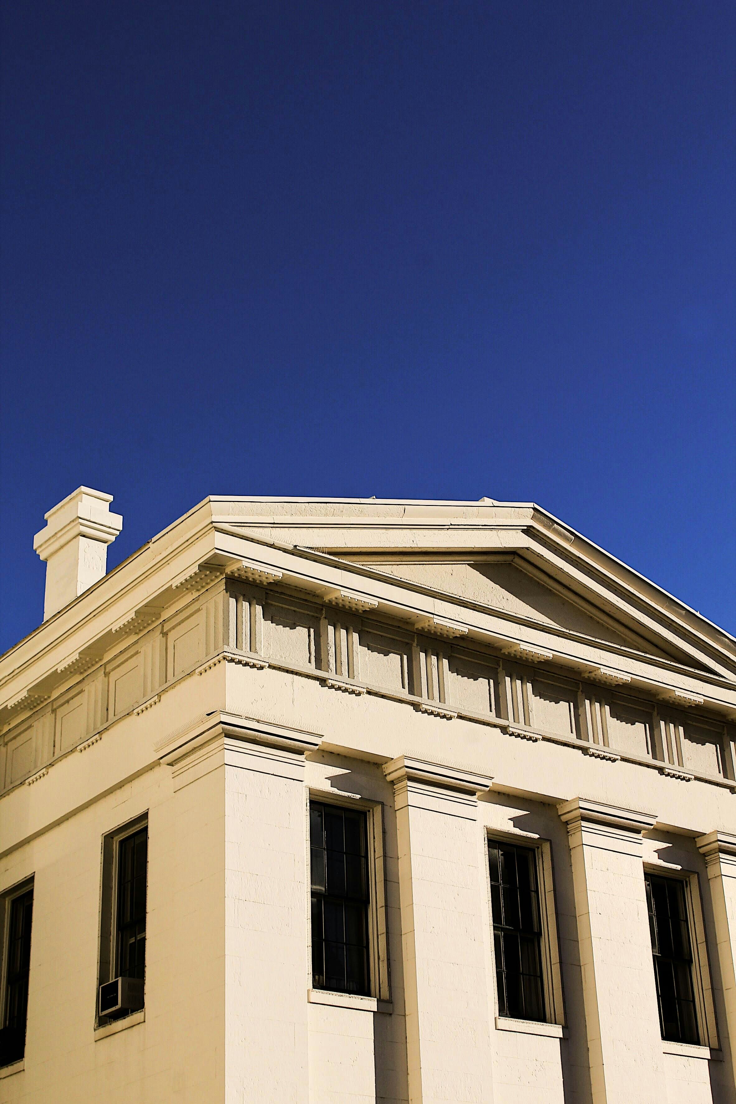 White classical building with intricate cornices and large windows, set against a clear blue sky.