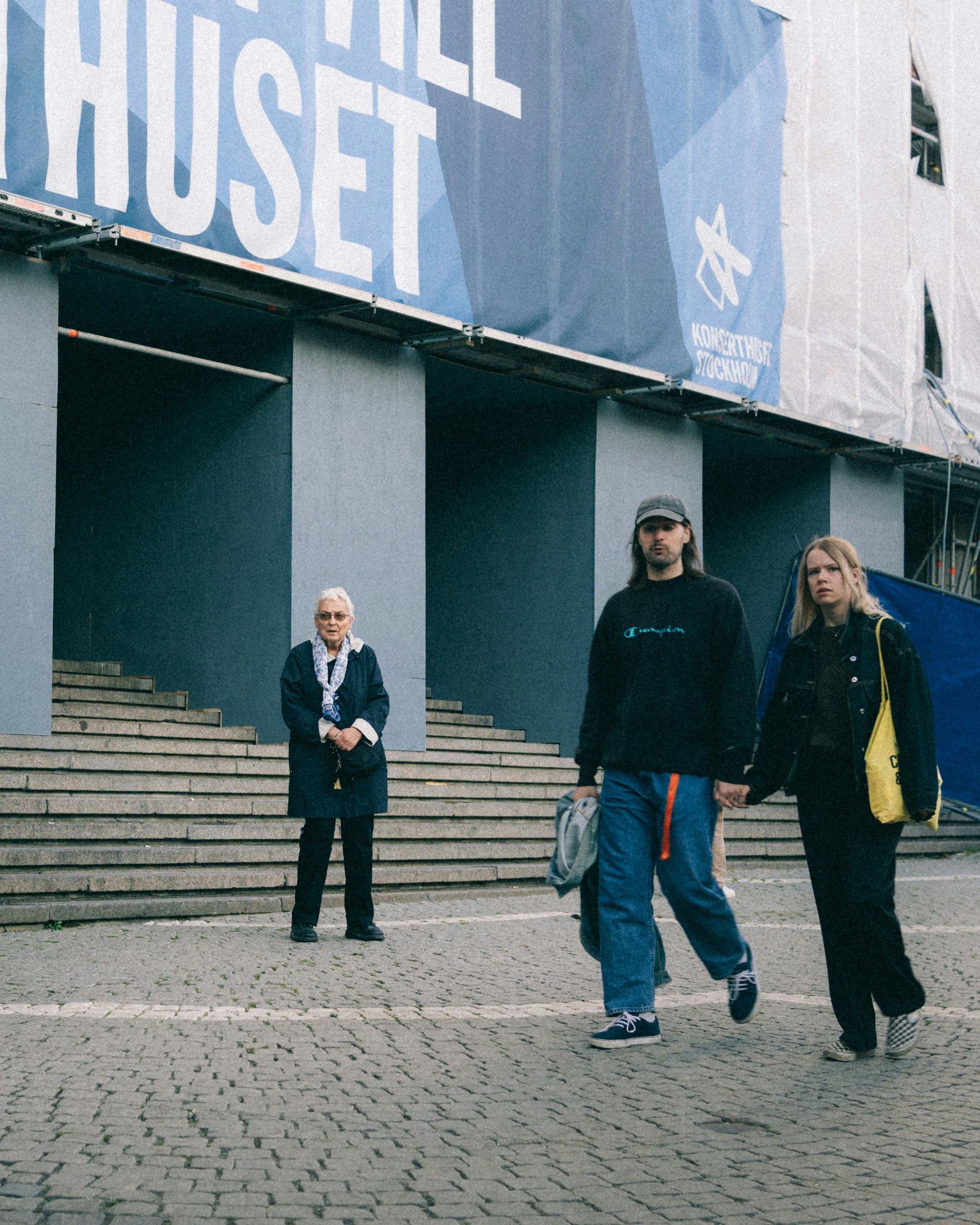 I don’t know who you were waiting for, or what was on your mind, but I hope it found its way when I walked away 🌱❤️ | Three people walk past a building with large text