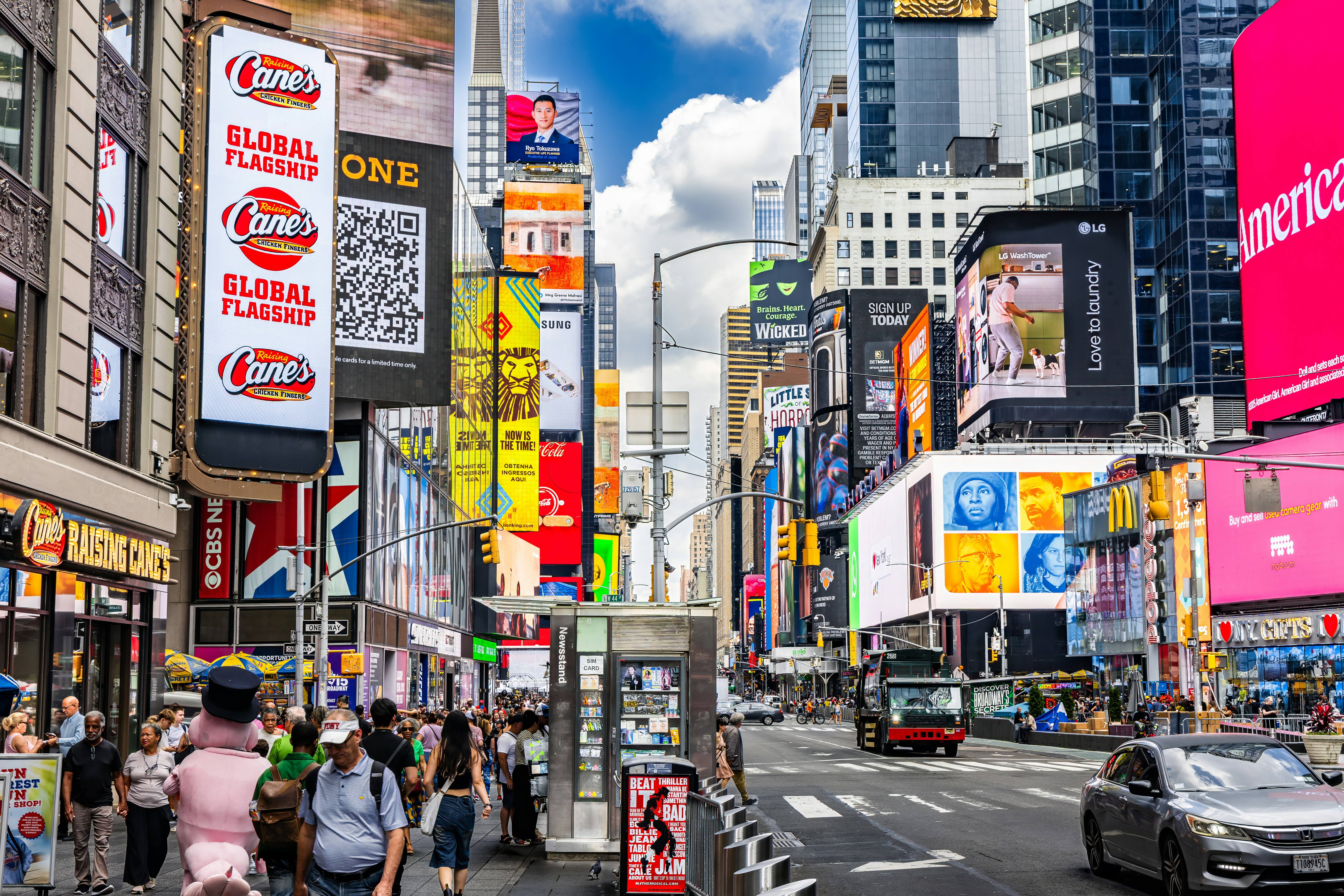 Times Square is a major commercial intersection, tourist destination, entertainment hub, and neighborhood in the Midtown Manhattan section of New York City. It is formed by the junction of Broadway, Seventh Avenue, and 42nd Street. Together with adjacent Duffy Square, Times Square is a bowtie-shaped plaza five blocks long between 42nd and 47th Streets. | Busy street scene with billboards in new york city.