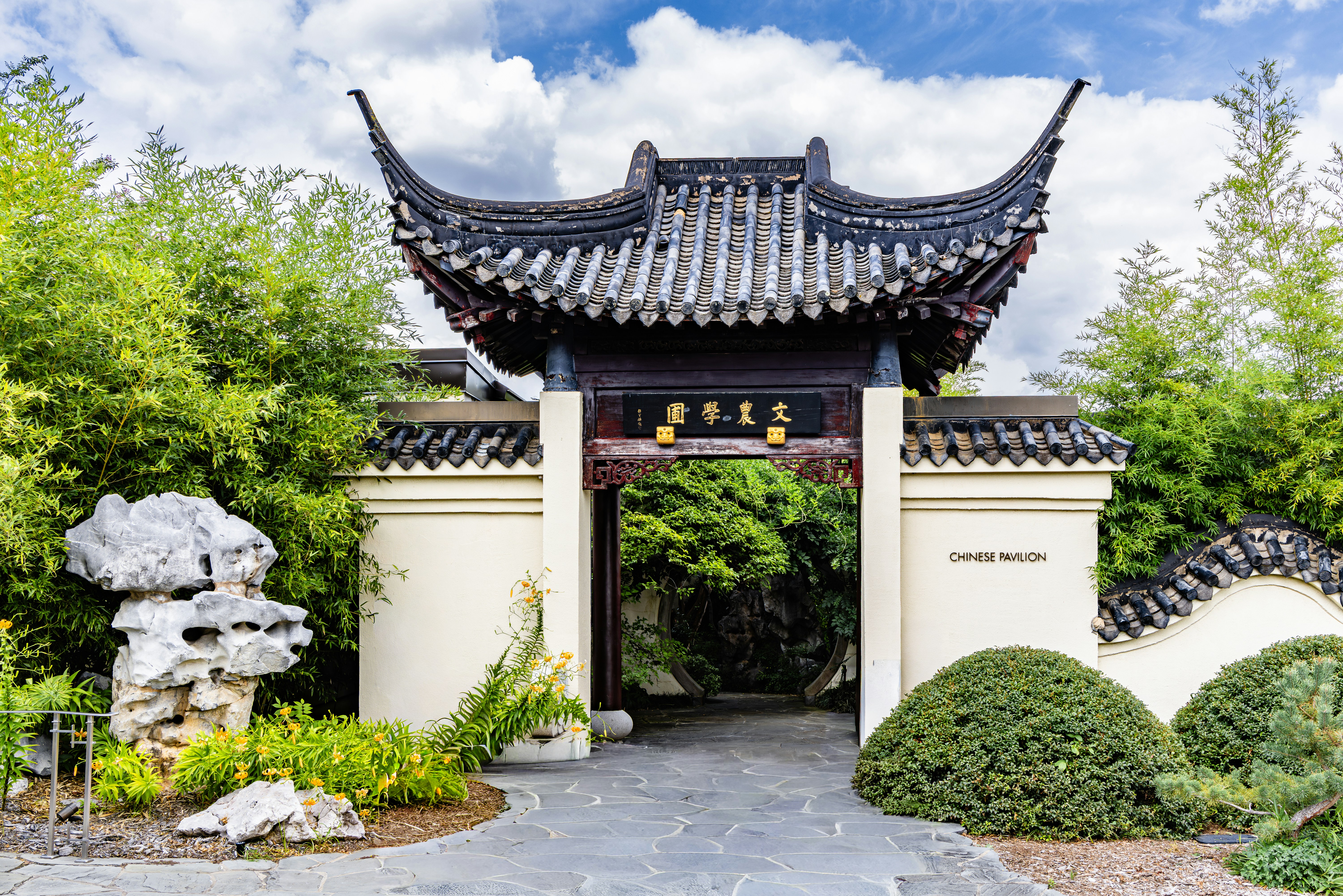 Tucked into Northeast DC, the United States National Arboretum is a 451-acre living museum of trees, shrubs, and botanical collections curated by the USDA. Established in 1927, it’s home to nine miles of winding roadways, sweeping meadows, and landmark features like the National Capitol Columns, which once graced the East Portico of the Capitol. Visitors can explore themed gardens including the Asian Collections, Fern Valley, and the National Herb Garden, or marvel at the world’s first museum dedicated to bonsai and penjing. With its blend of scientific research, horticultural beauty, and cultural history, the Arboretum offers a serene escape and a rich canvas for exploration. | Traditional chinese gate with lush greenery and blue sky