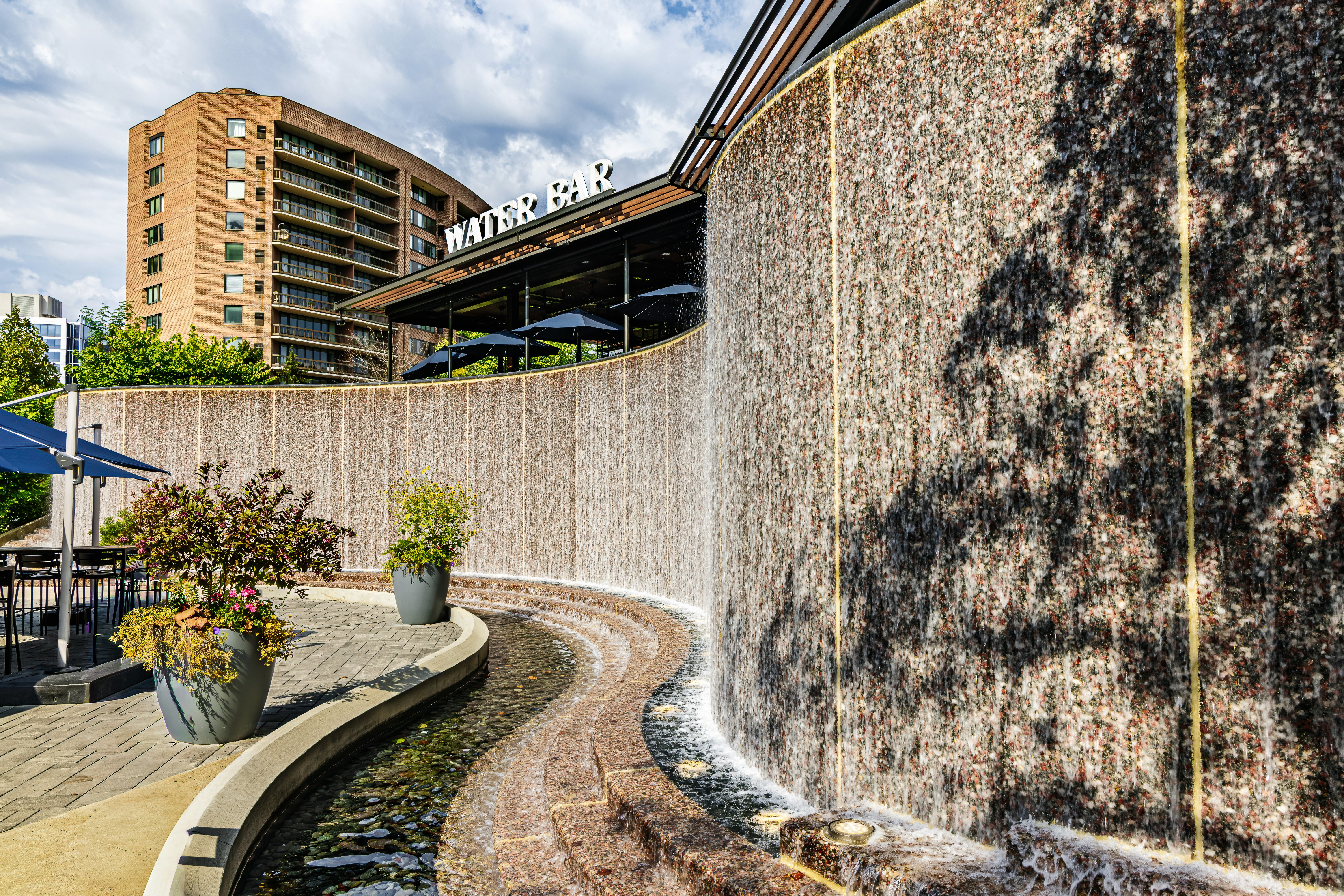 Water Park on Crystal Drive in Arlington, VA. | Curving waterfall wall with a small stream and building.