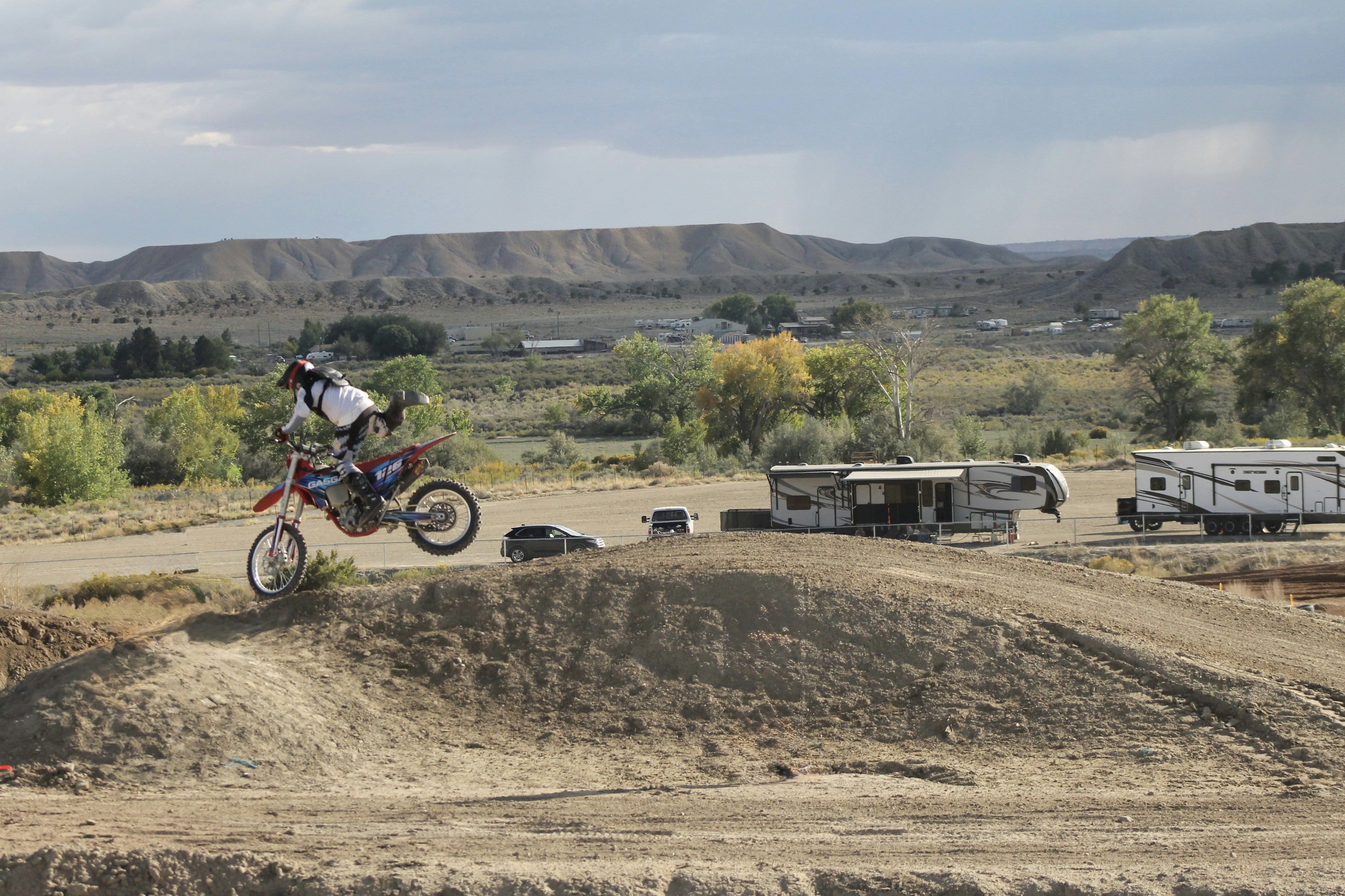 Motocross rider jumps over dirt mound with campers in background