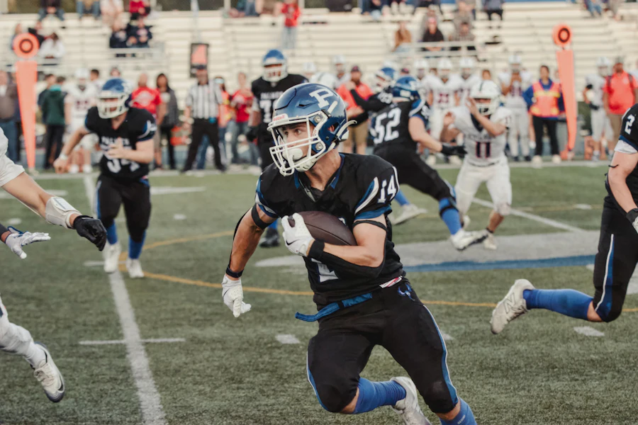 No.14 clutching the ball while cutting through defenders on a turf football field during live play.