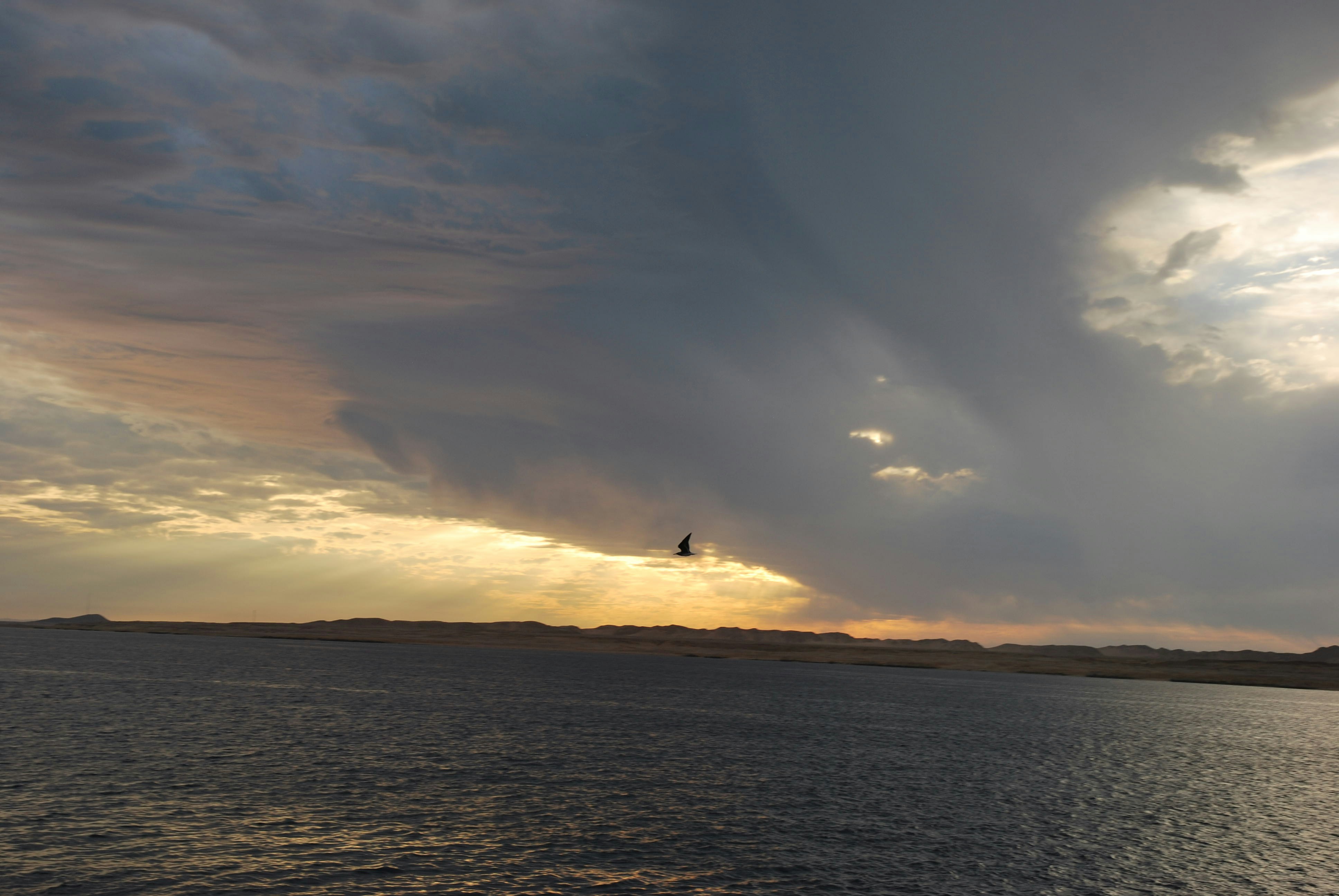 Dramatic sunset over the ocean with a distant helicopter.
