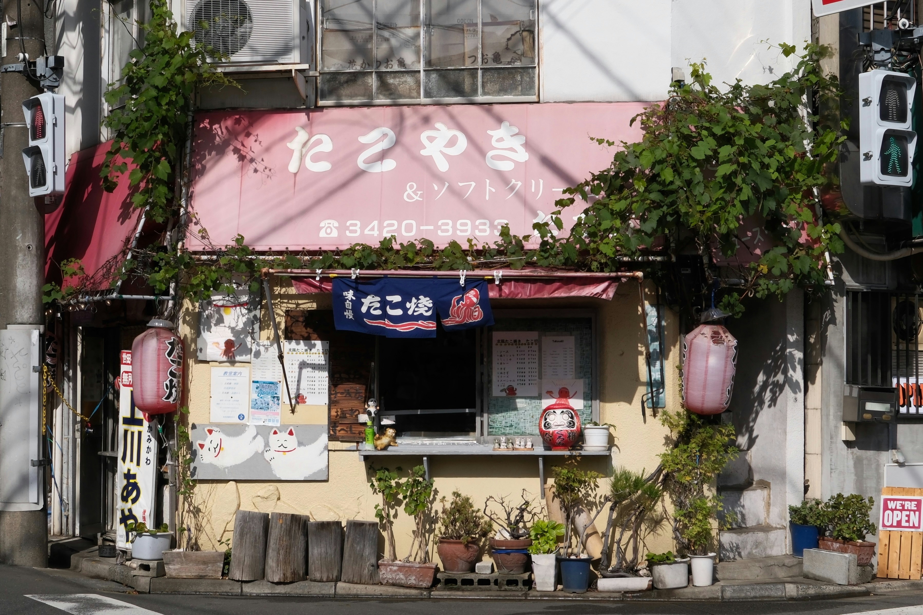 A cozy eatery adorned with pink awnings and lush vines, featuring traditional lanterns and a welcoming sign. The scene captures the essence of local culinary culture.