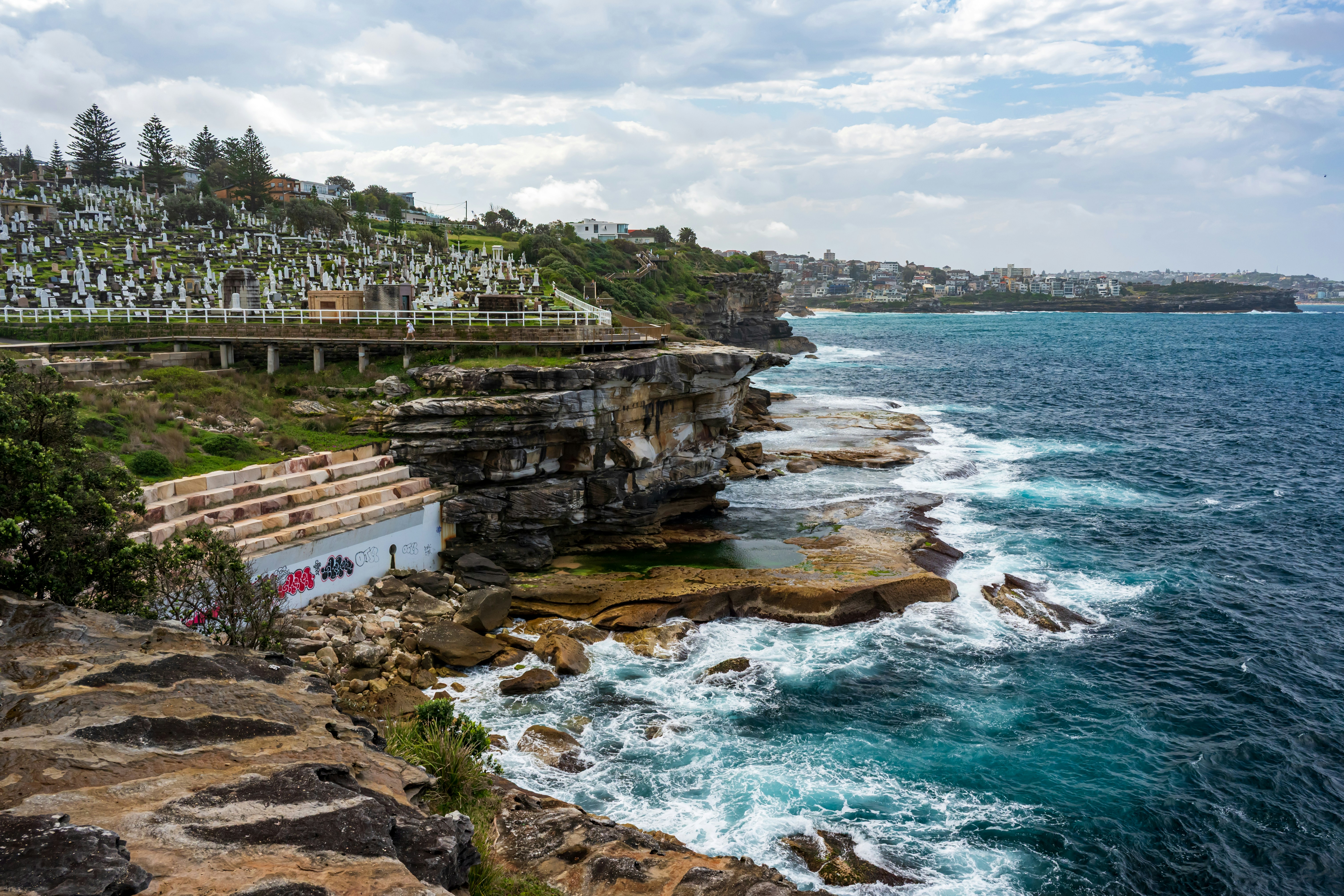 Rocky coastline with ocean waves and cemetery above ground cemetery.