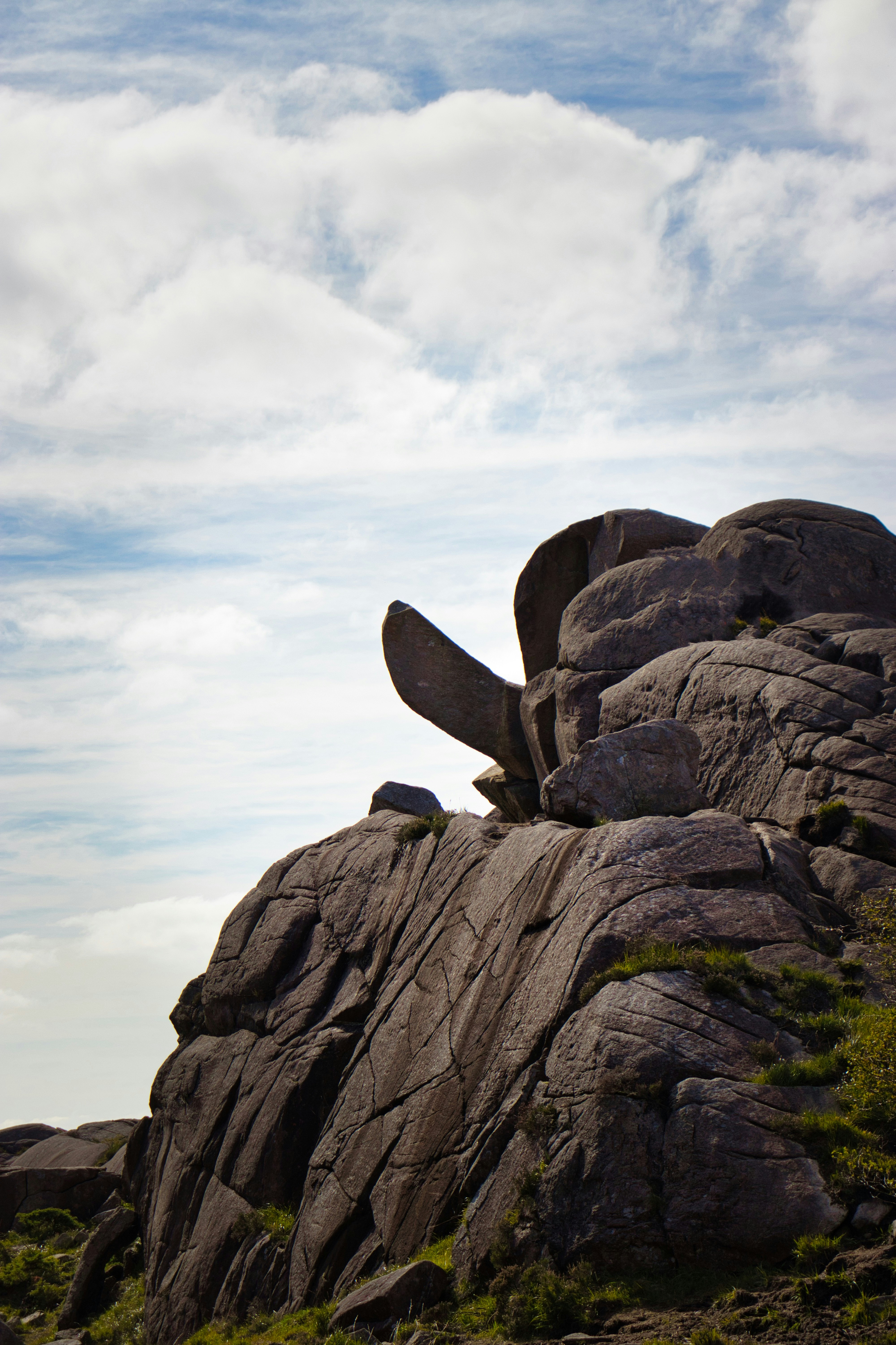 Large rock formation resembling a whale tail against a blue sky with scattered clouds.
