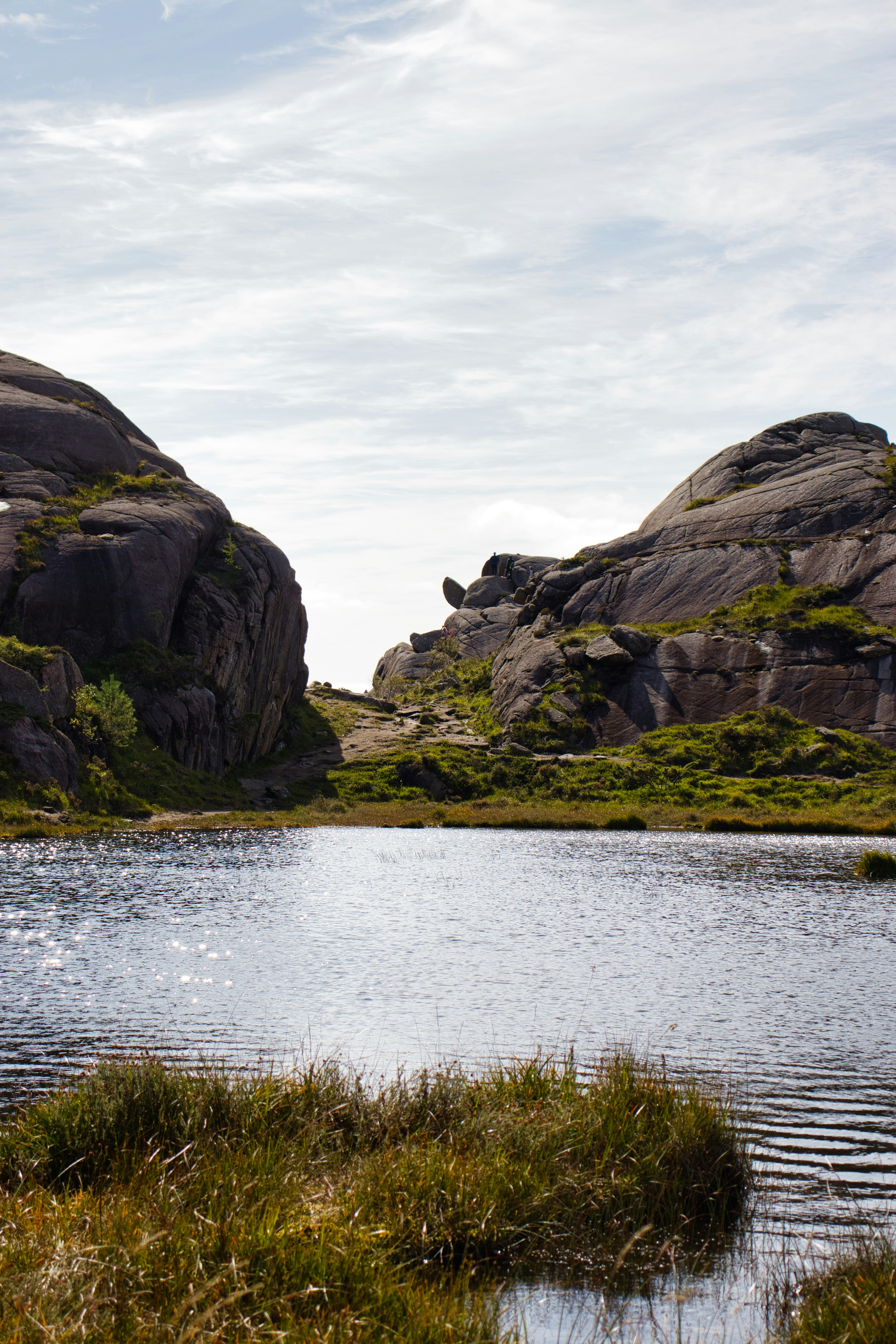 Lush green landscape flanked by towering rocks, with a tranquil pond reflecting the sky. The scene evokes a sense of calm and natural beauty.