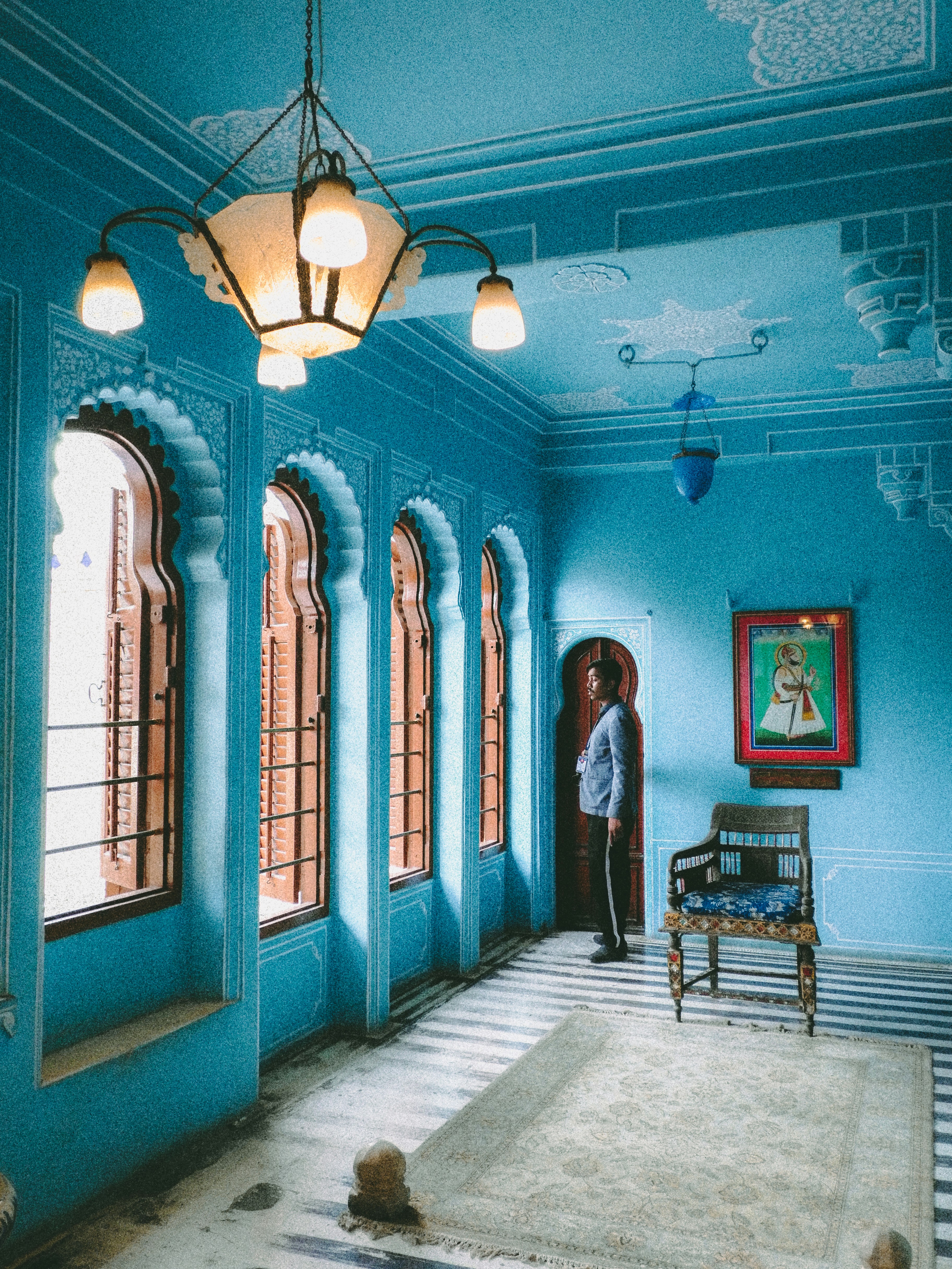 Man in blue room with arched windows and ornate decor.