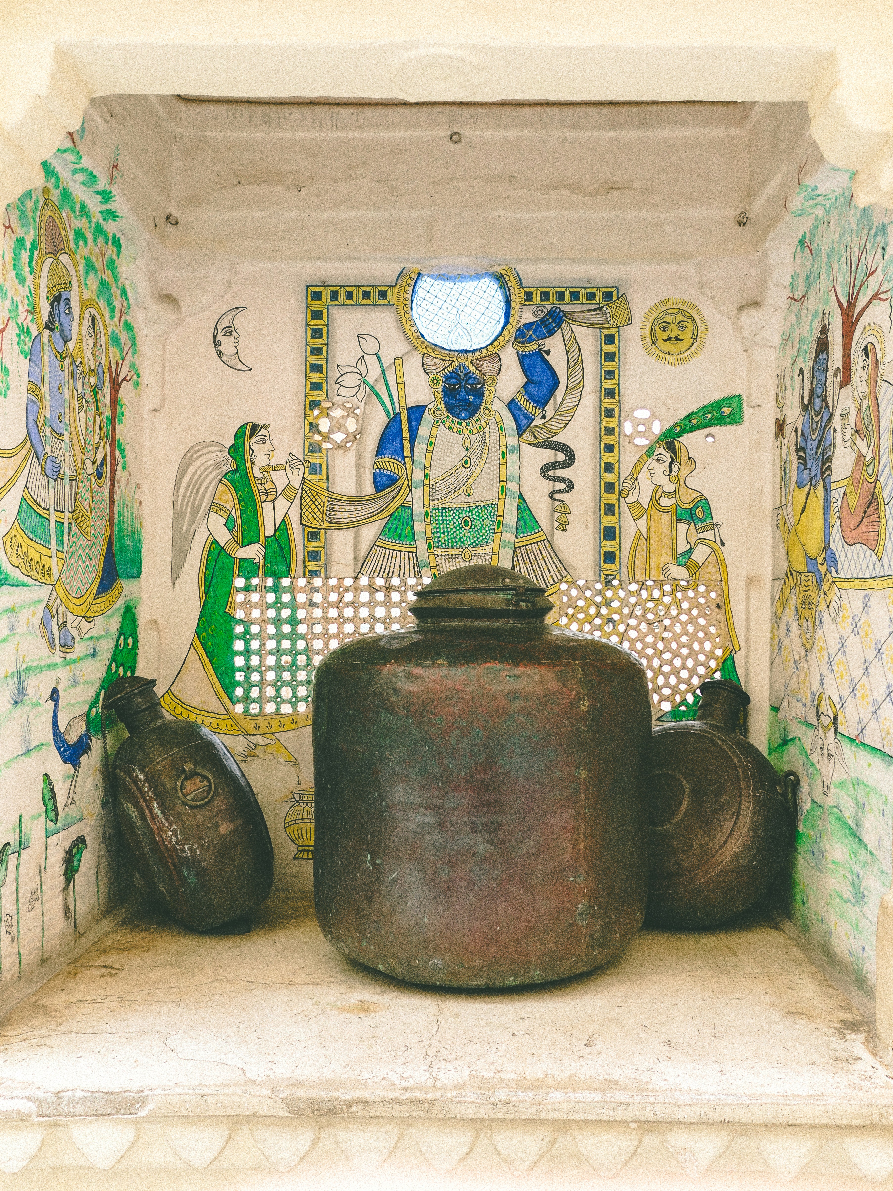 Three antique pots displayed with colorful wall paintings.