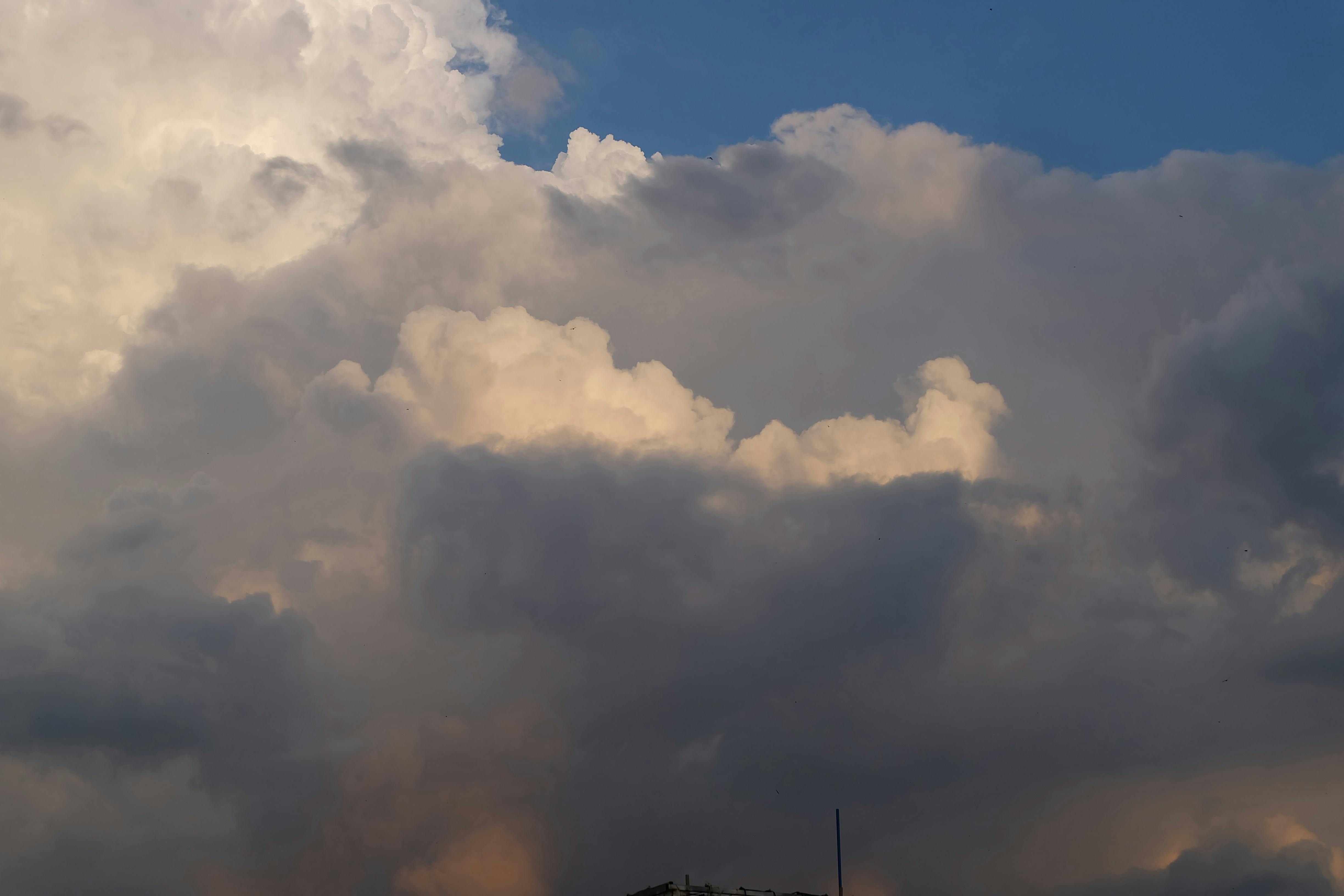 Dramatic clouds illuminated by sunlight against blue sky.