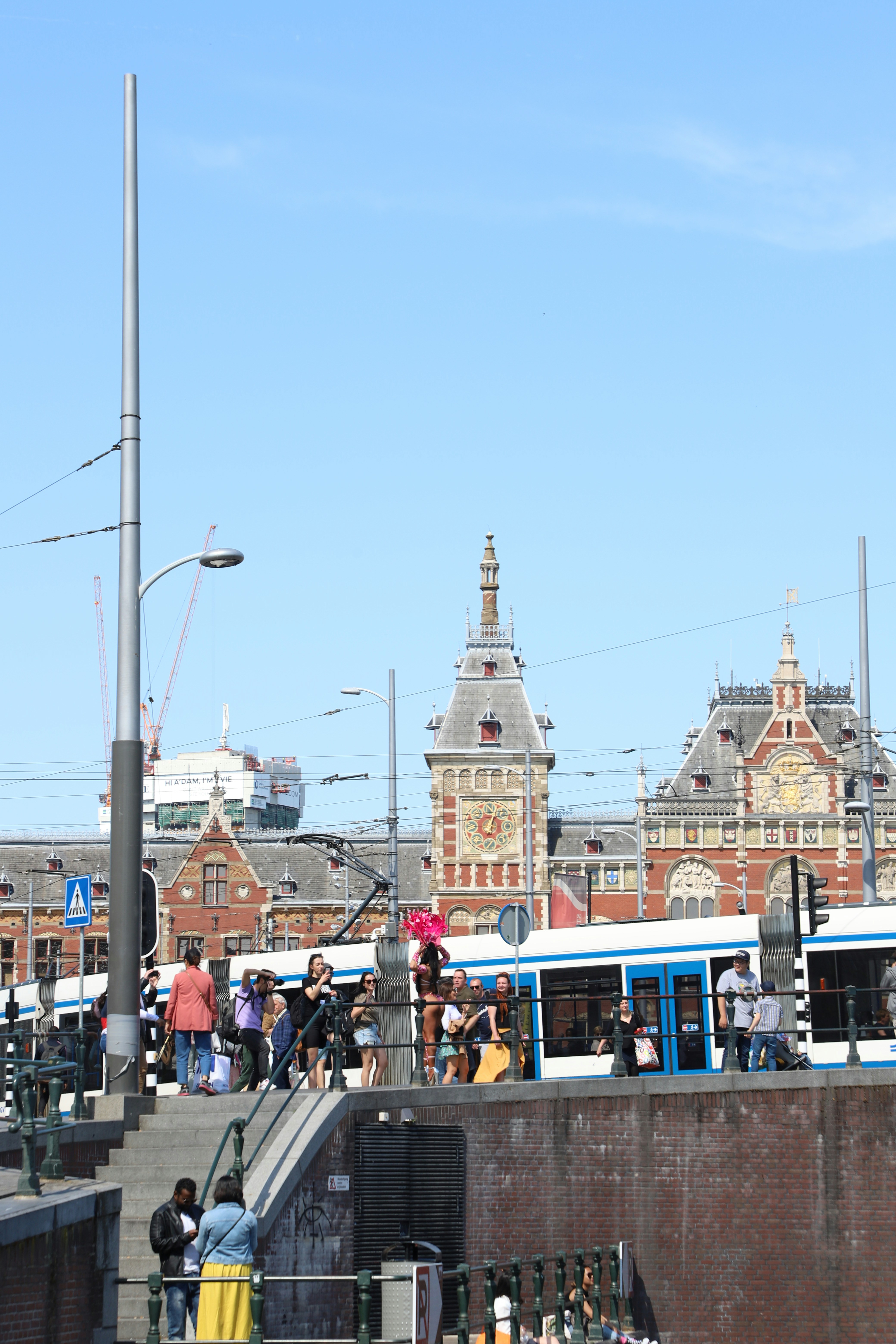 People on a bridge with tram and historic buildings.