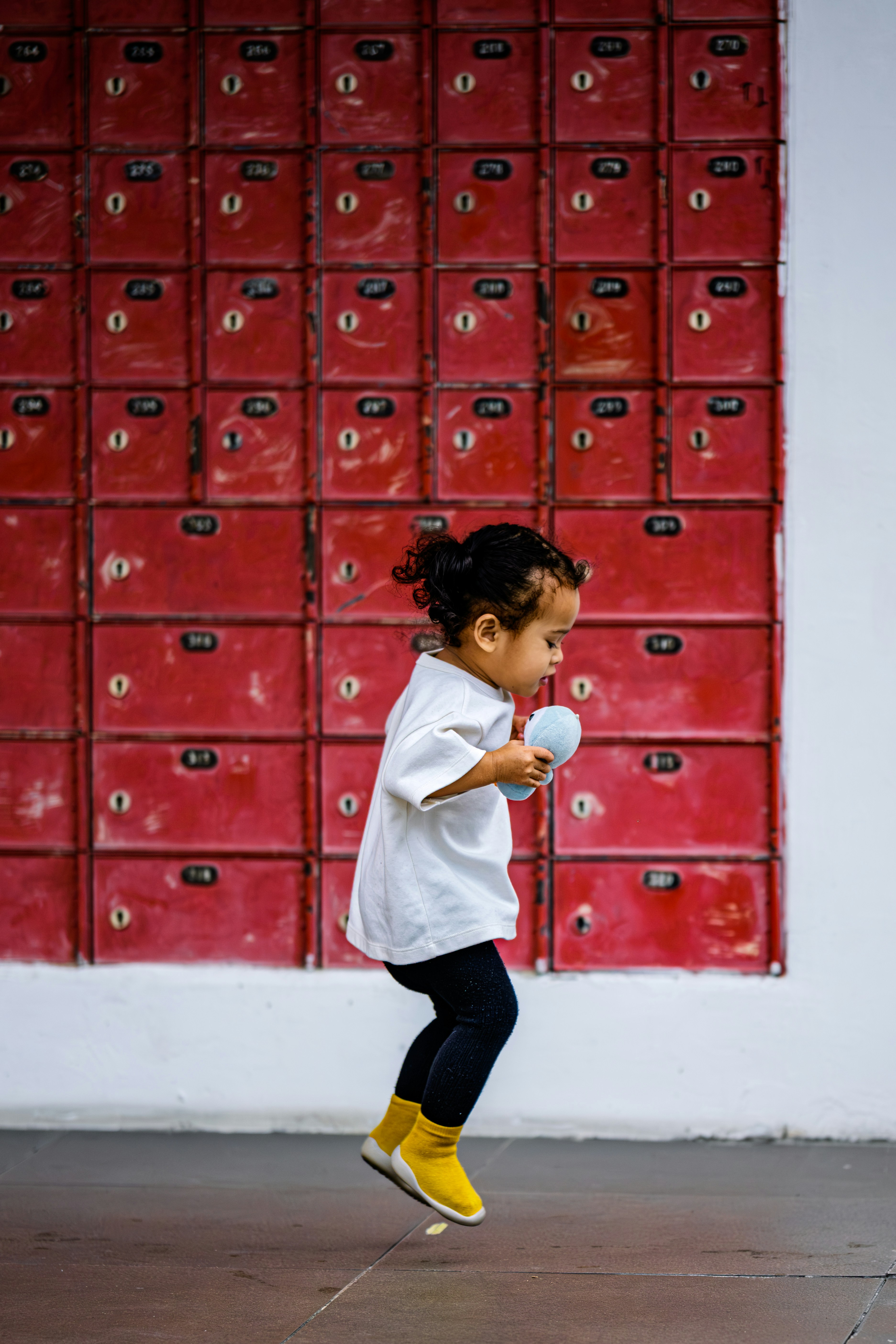 never goes anywhere without her penguin toy. | Young girl jumps rope in front of red lockers.