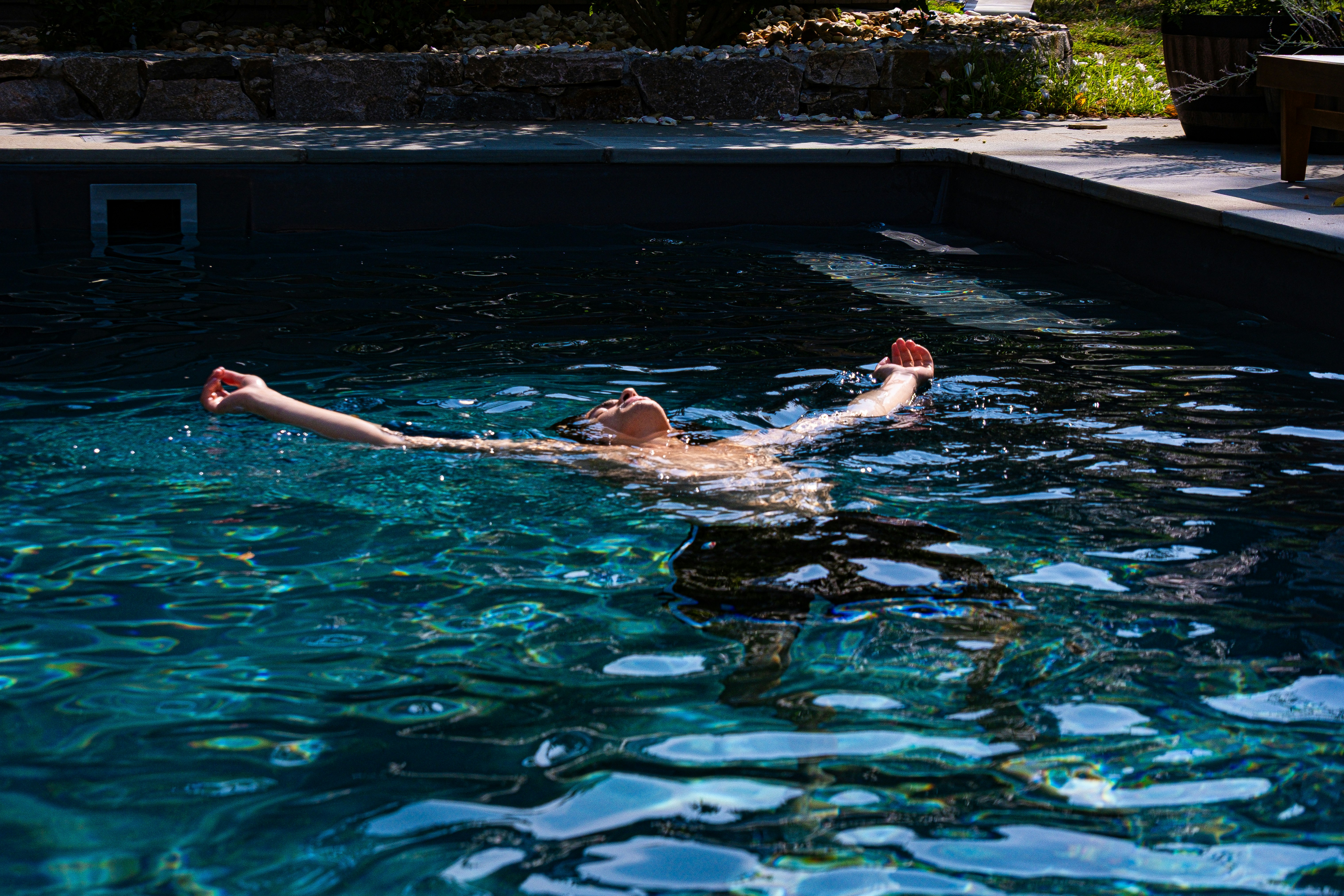 floating in pool | A person swims in a clear blue swimming pool.