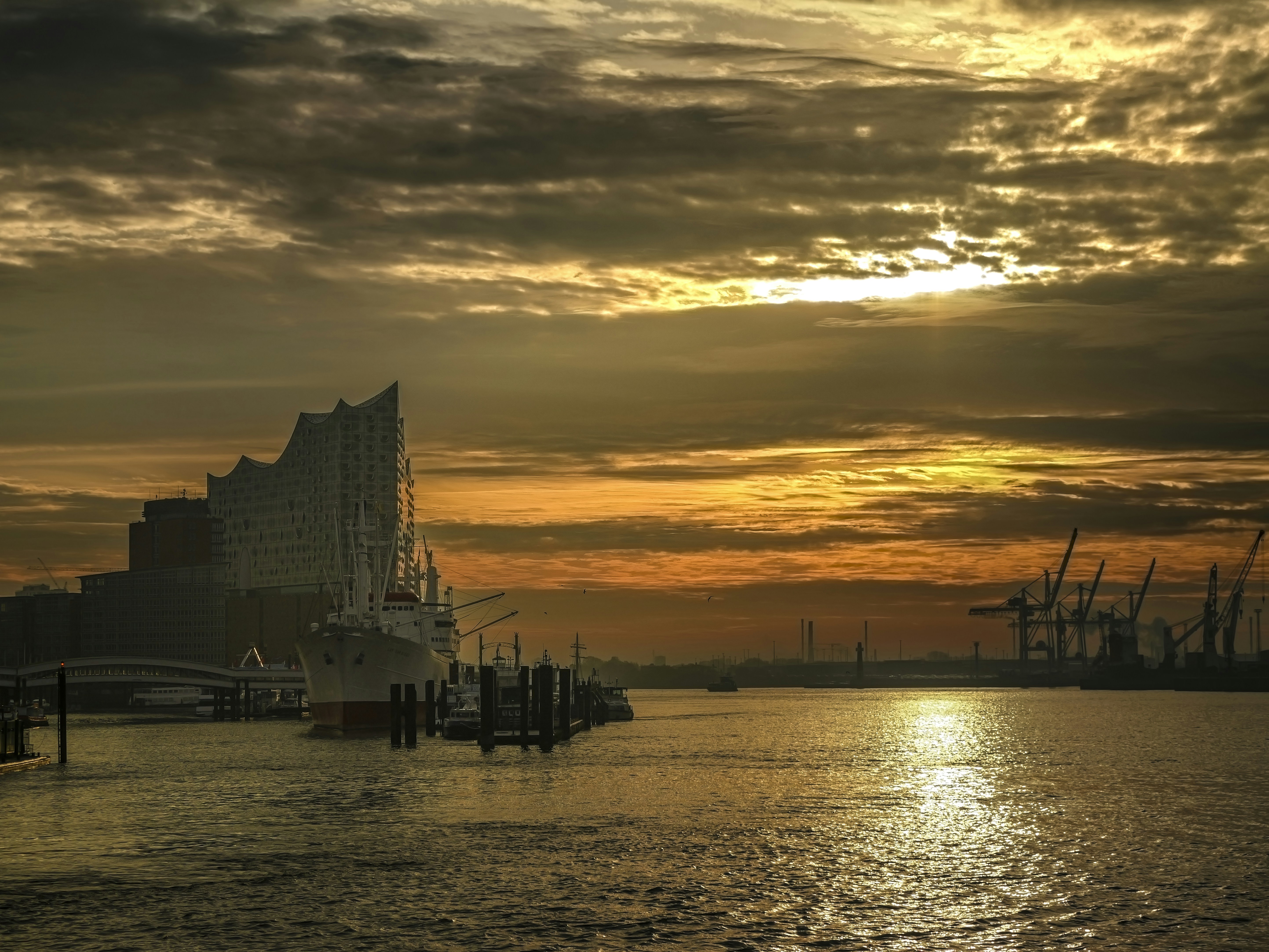 Harbor with cranes and building at sunset.
