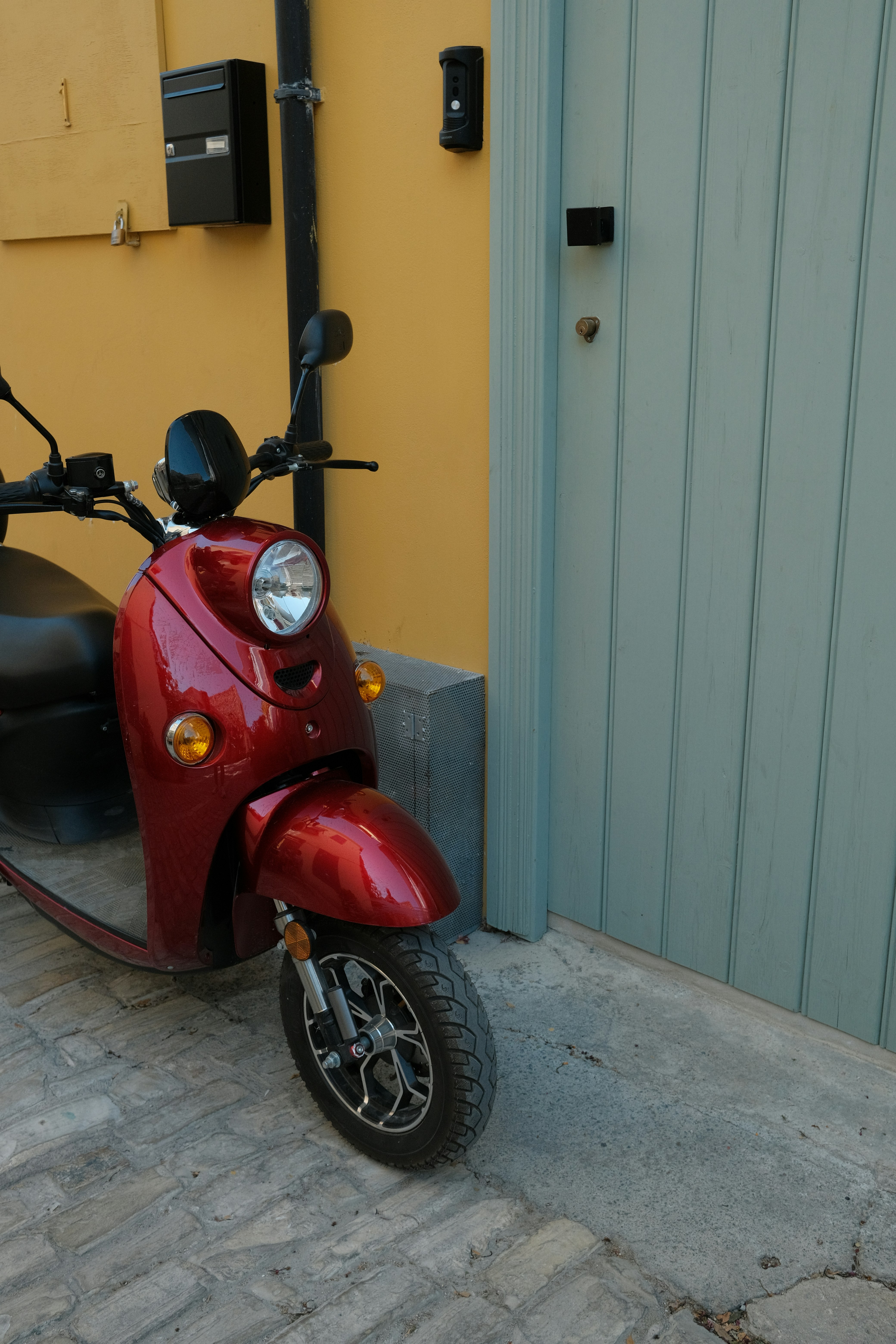 Red scooter parked next to a light blue door.
