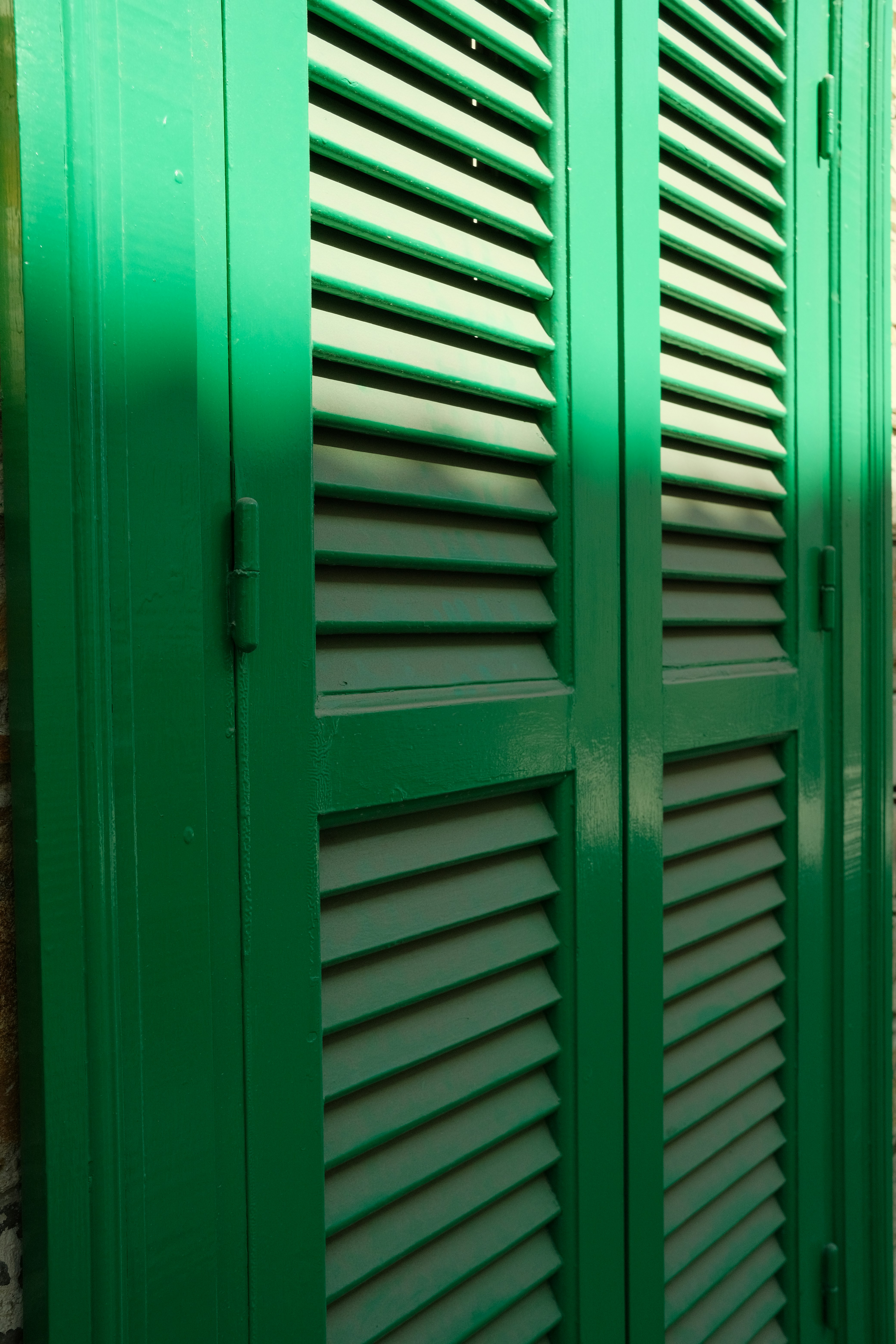 Green louvered shutters on a brick wall.