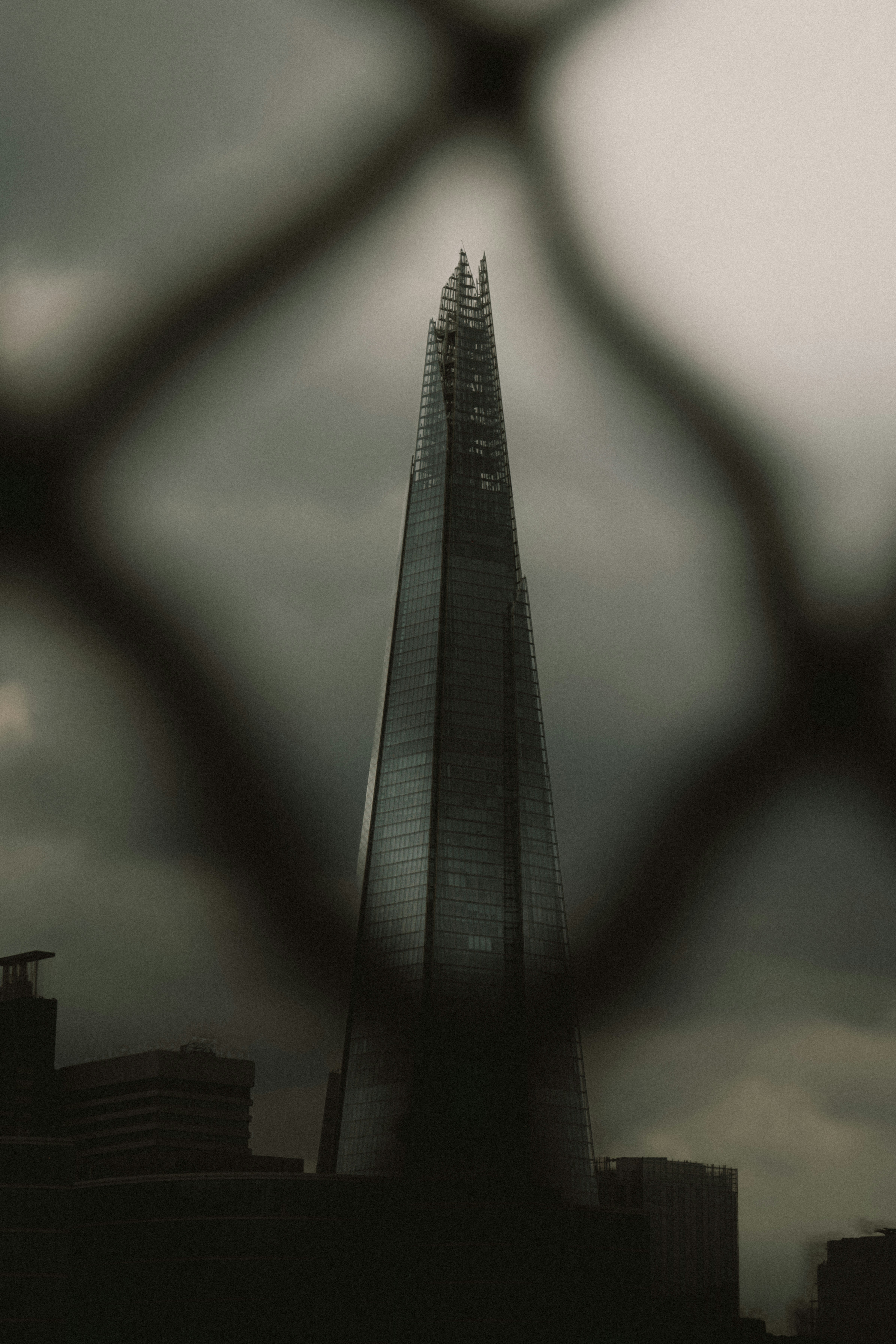 The shard 3/4 | Tall glass skyscraper viewed through a fence.