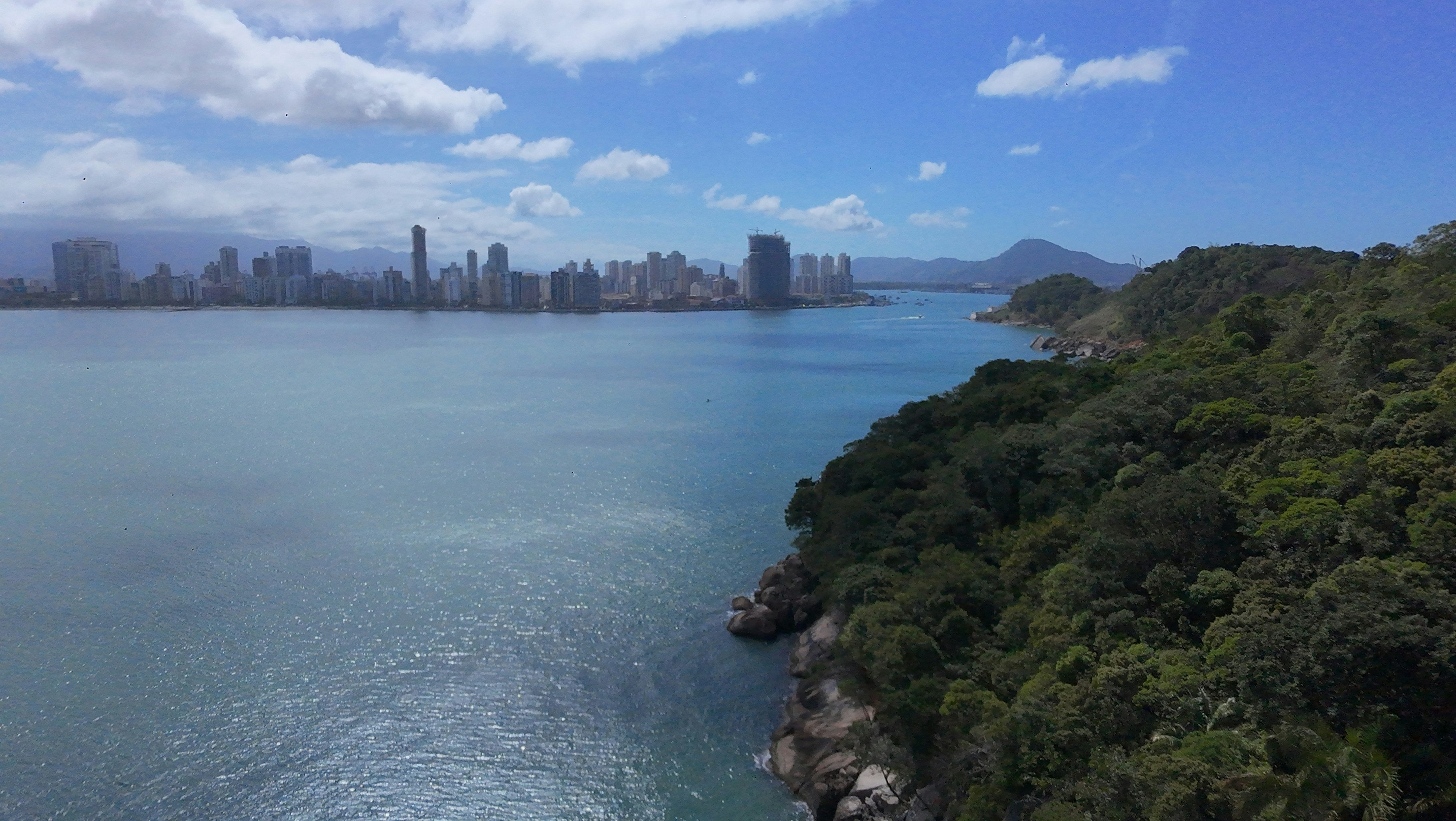Coastal city skyline with lush green hills and ocean.