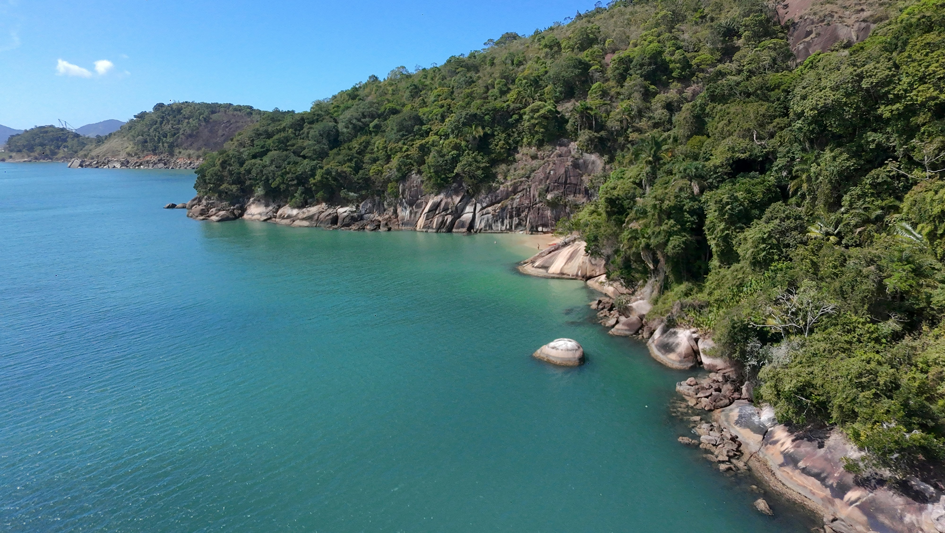 Turquoise ocean water meets a rocky, tree-covered coastline.