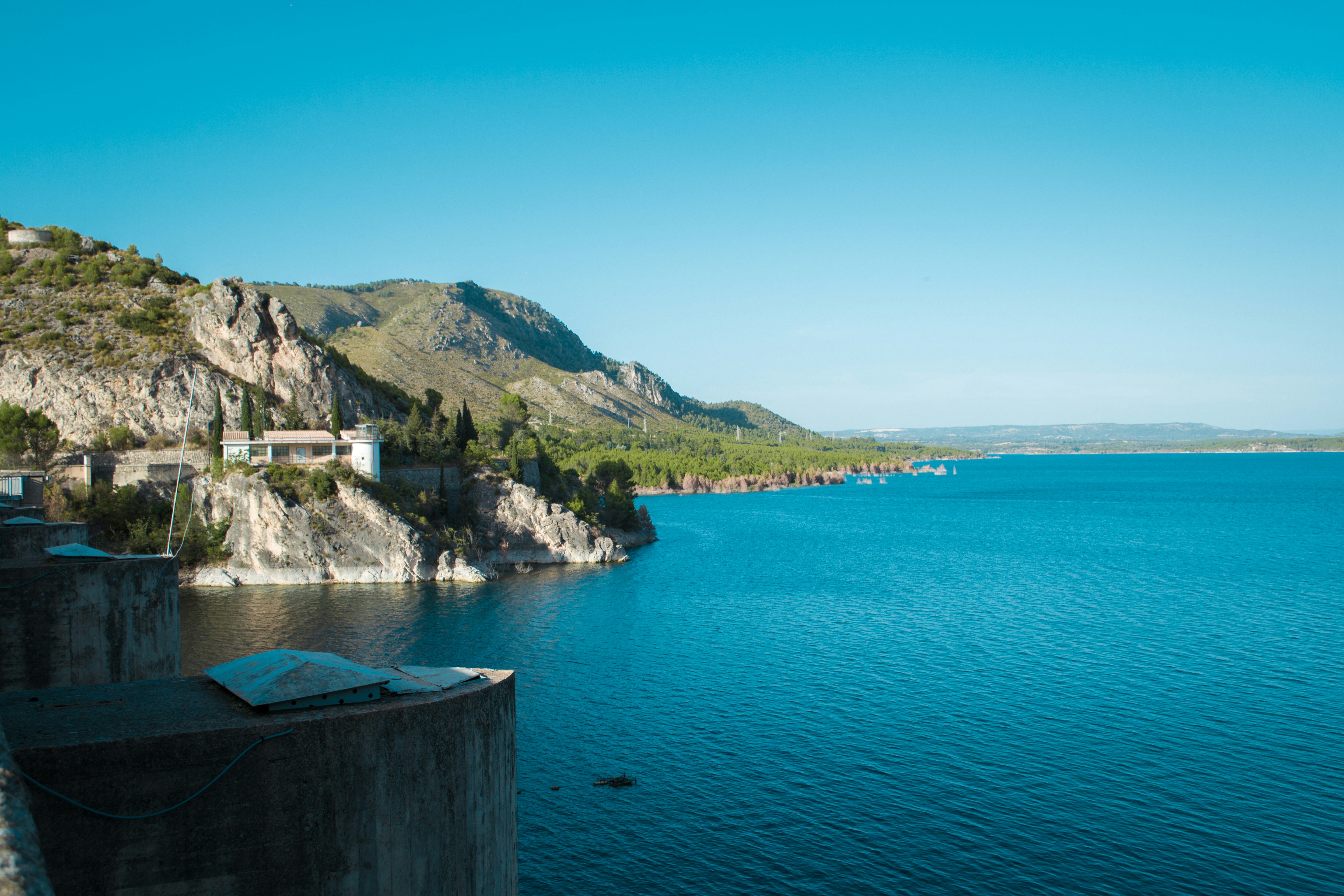 Tranquil lakeside view featuring rocky cliffs and lush greenery under a clear blue sky.