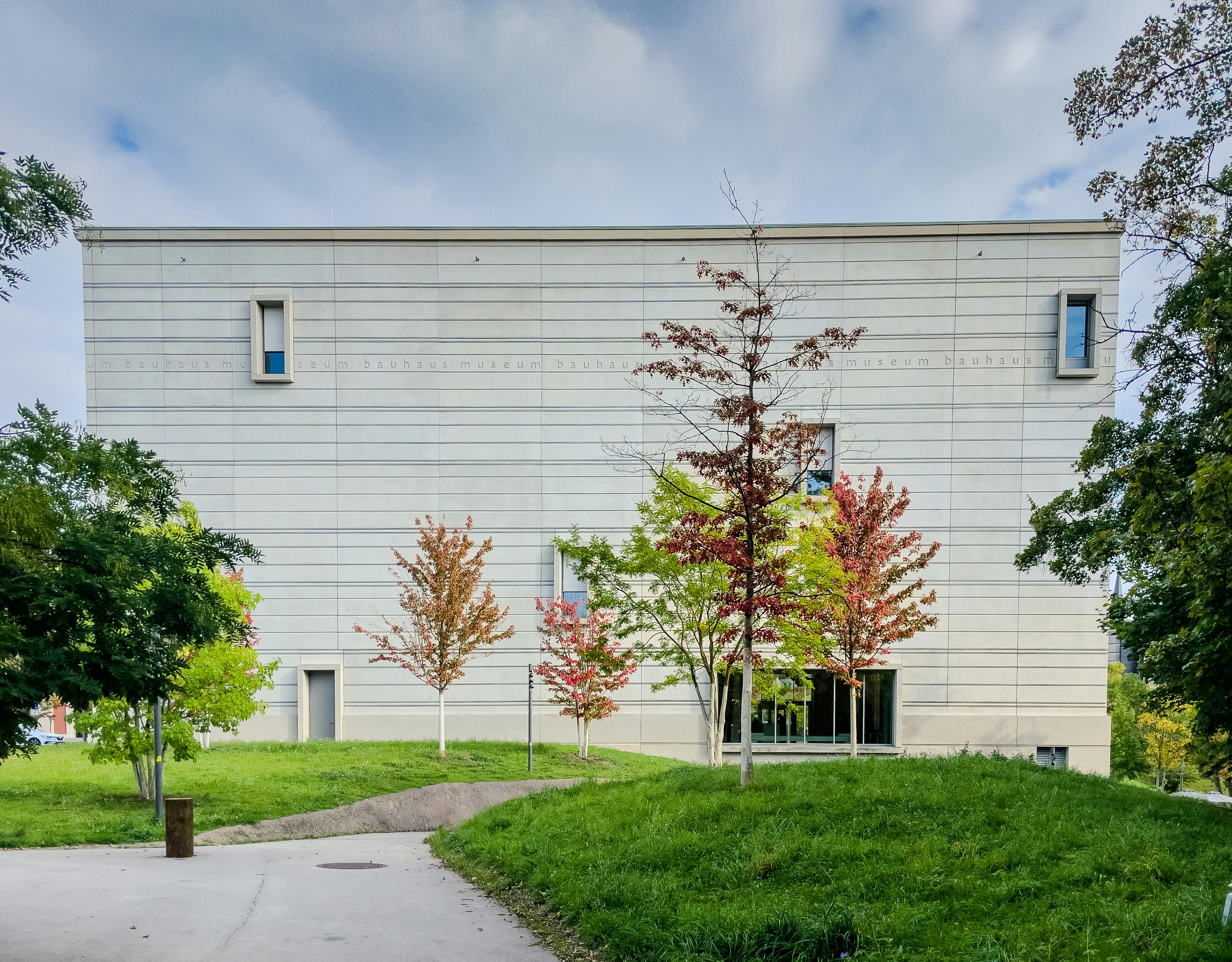 Modern concrete building with trees and grassy hill.