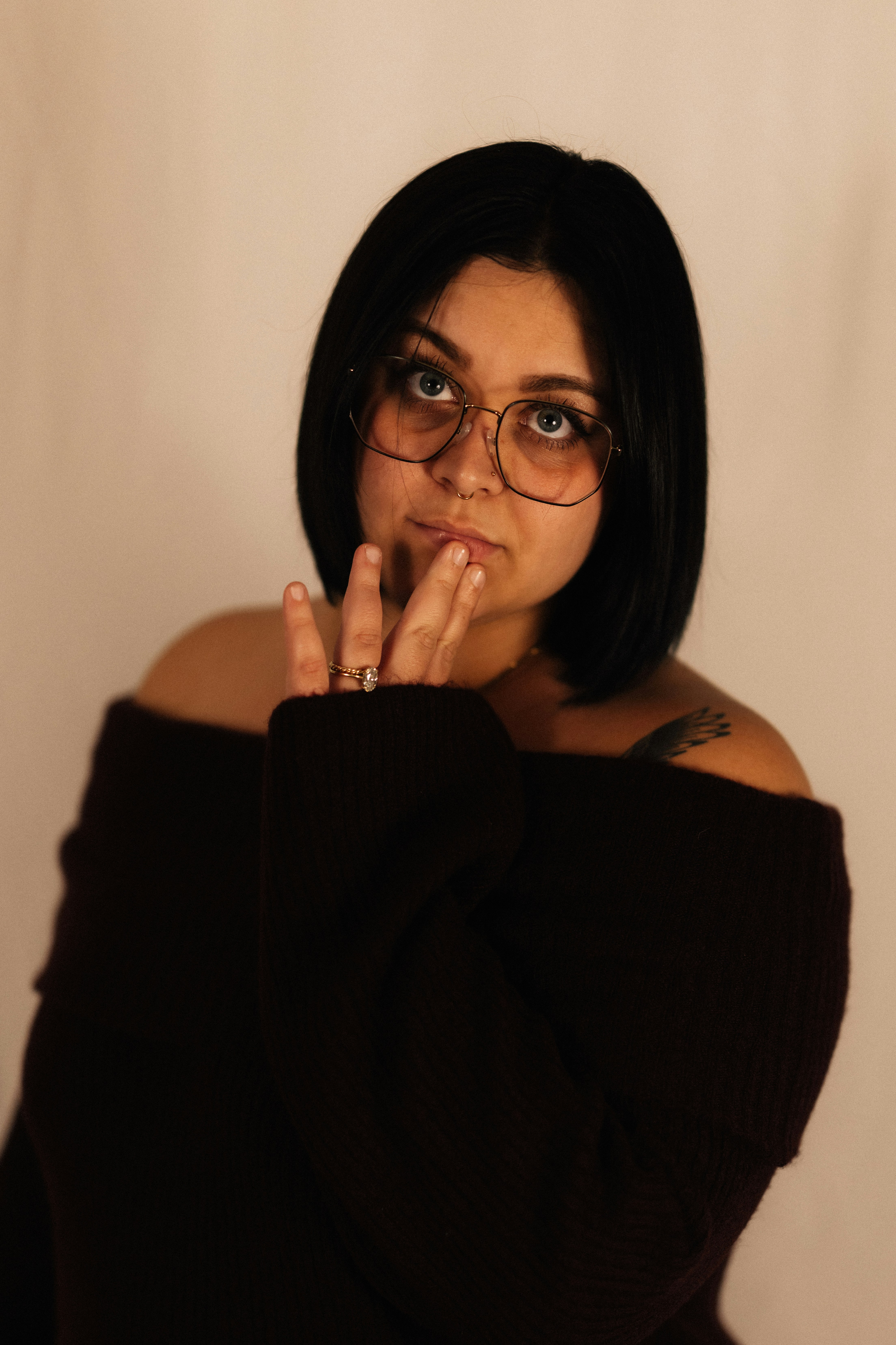 Woman with short dark hair and glasses touching face.