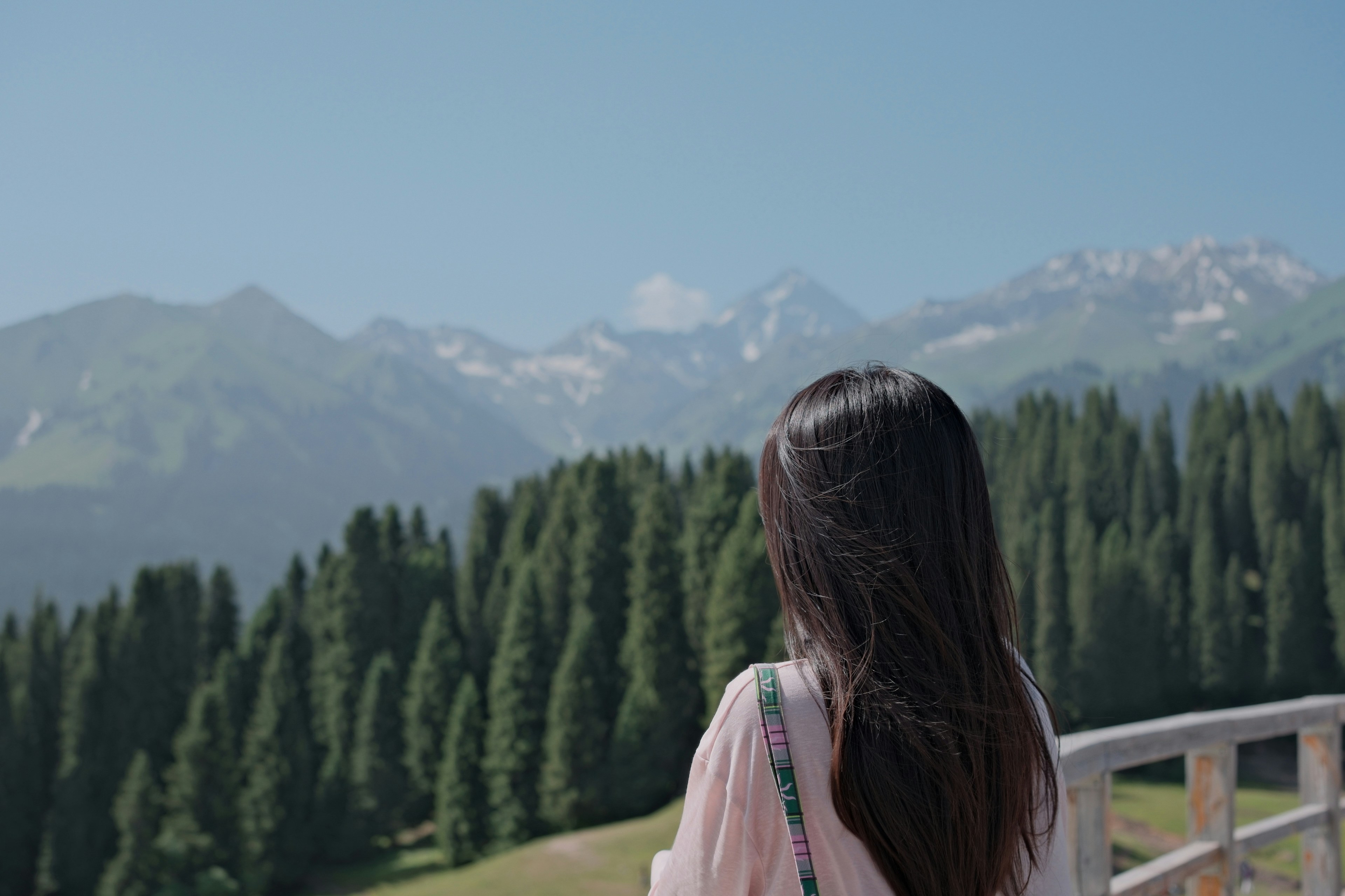A woman gazes at majestic mountains enveloped in lush greenery, embodying a moment of tranquility and reflection.