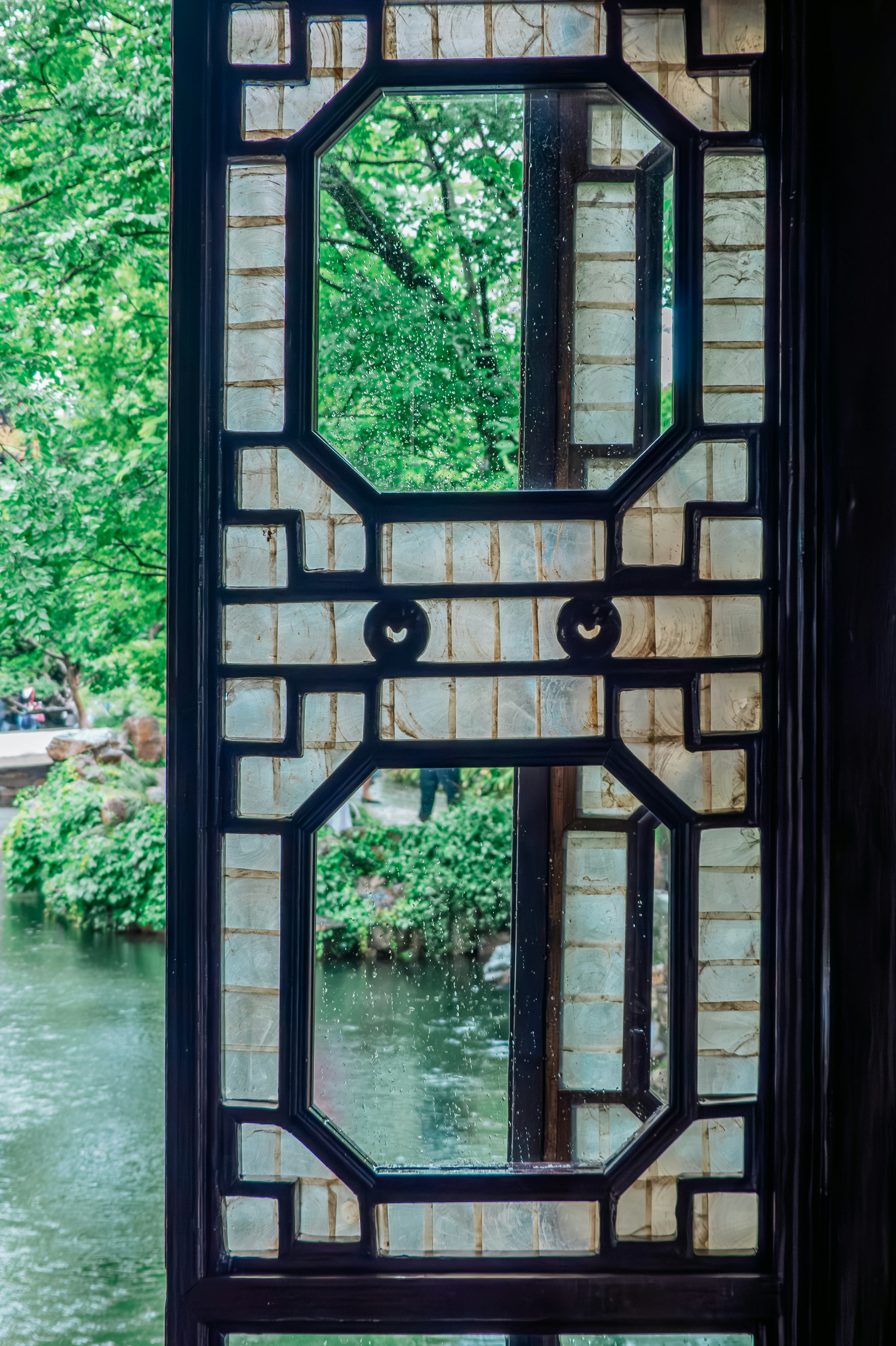 Ornate window overlooking a tranquil garden and water.
