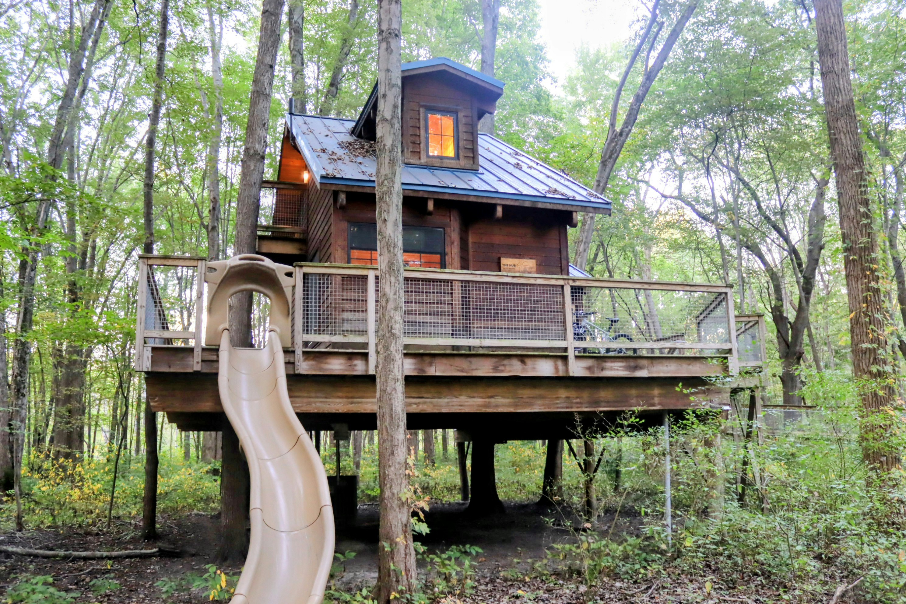 Charming treehouse nestled among tall trees, featuring a slide and a cozy balcony. Perfect for imaginative play and relaxation.