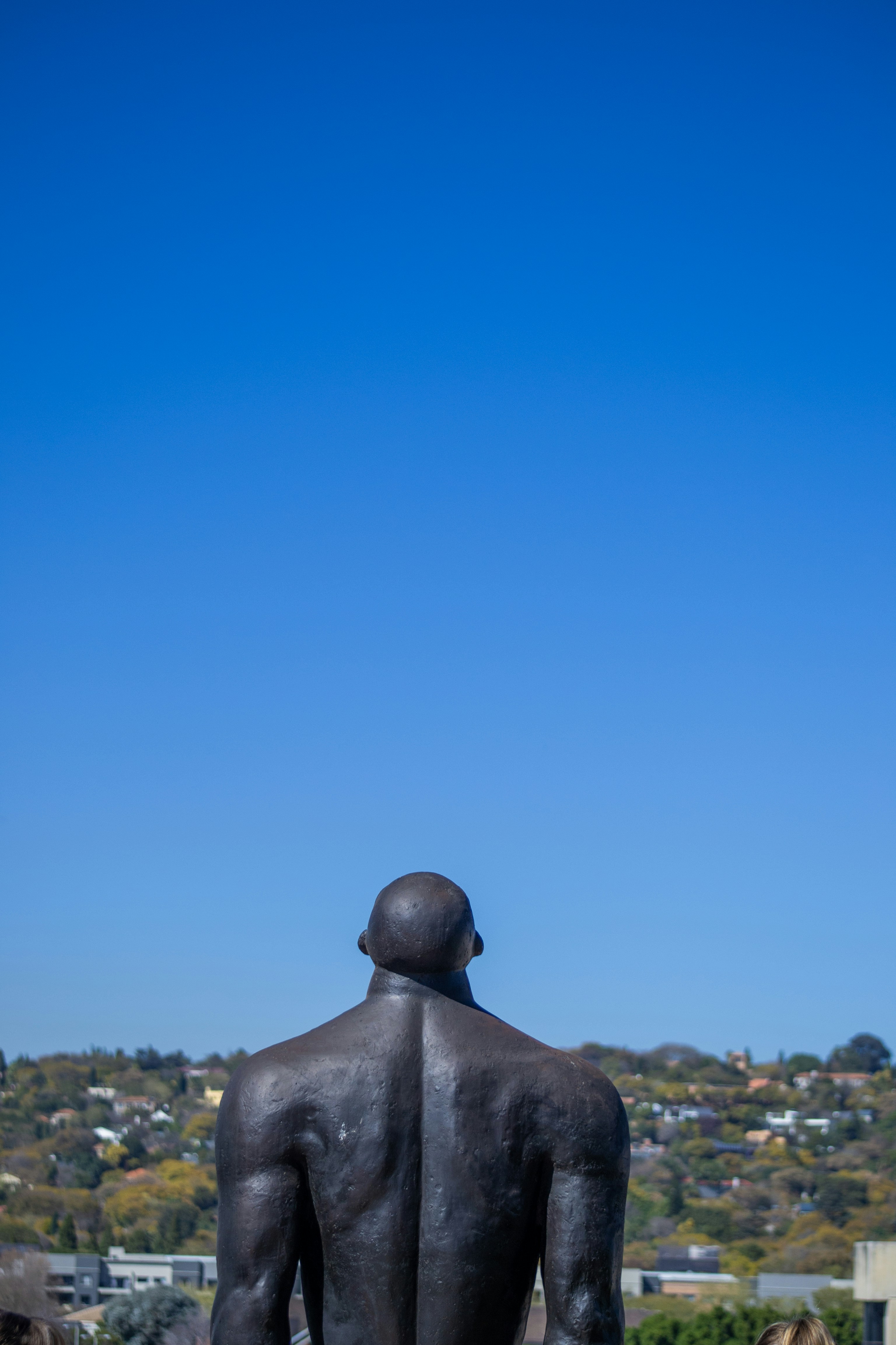 Bronze sculpture of a figure gazing into the distance, set against a vivid blue sky and rolling hills in the background.