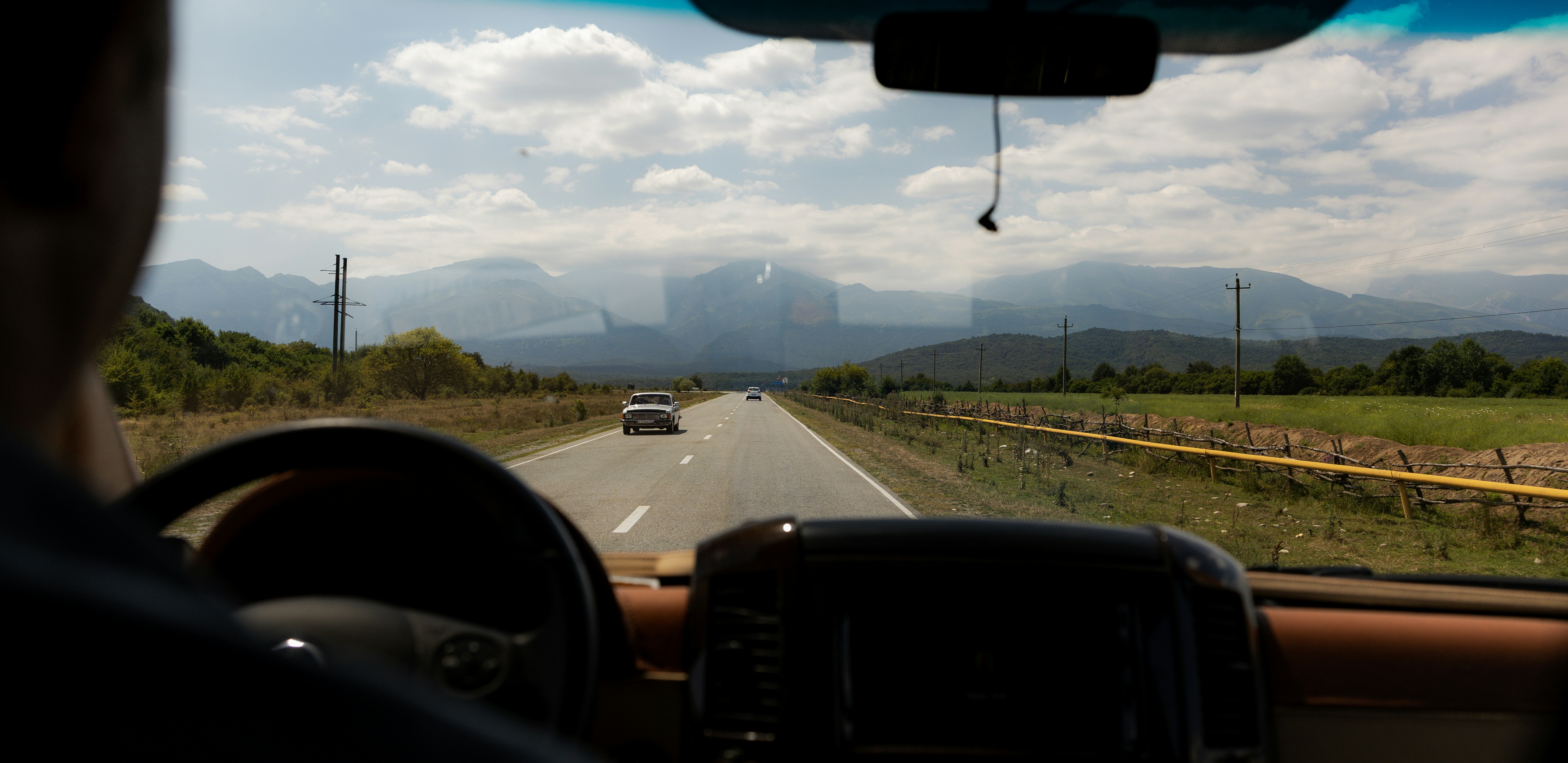 View from inside a vehicle looking down a highway with mountains in the background and a clear sky. The scene captures the essence of travel and adventure.