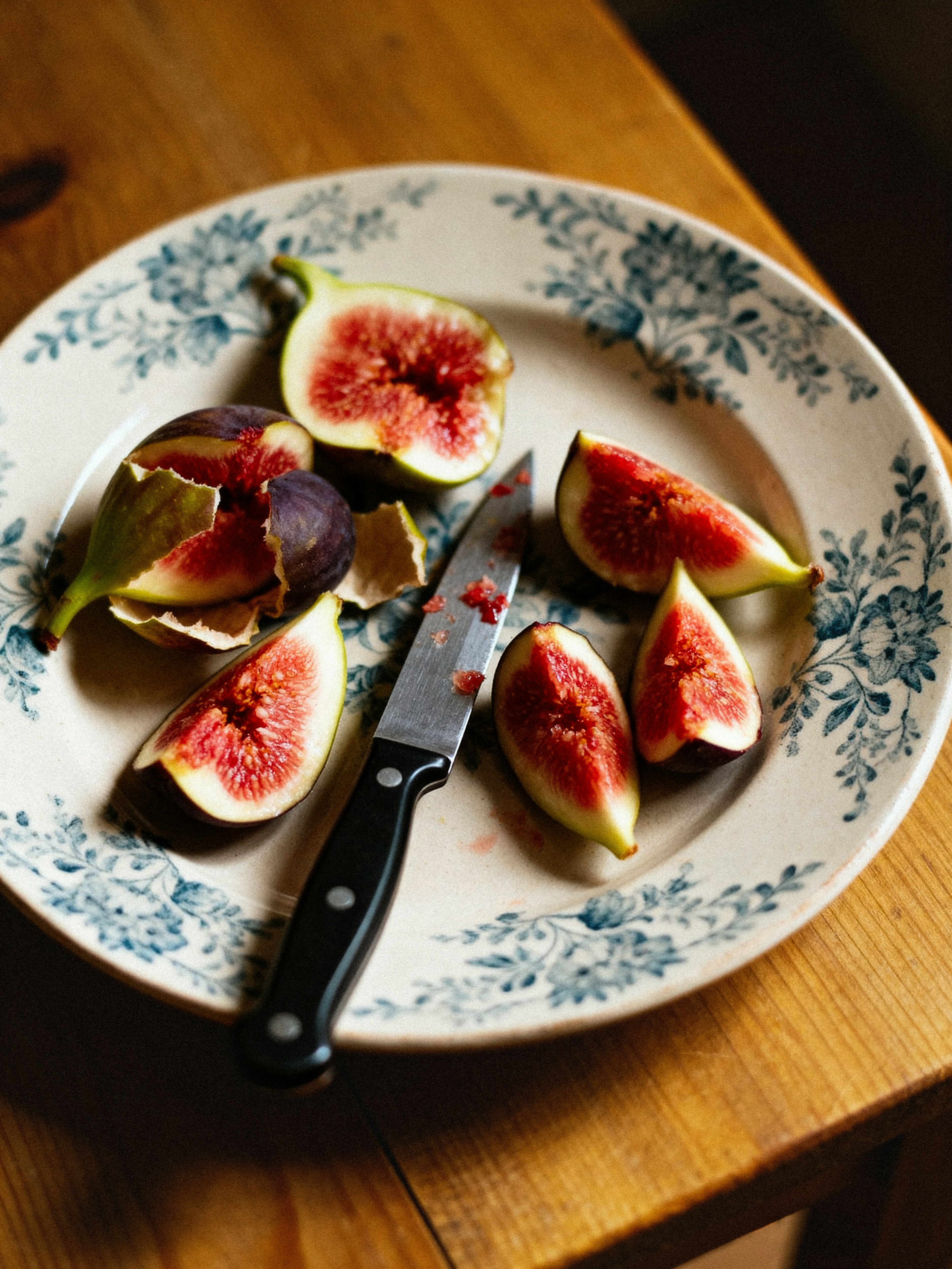 Sliced figs arranged on a vintage plate, accompanied by a small knife, showcasing the fruit's rich interior and texture.