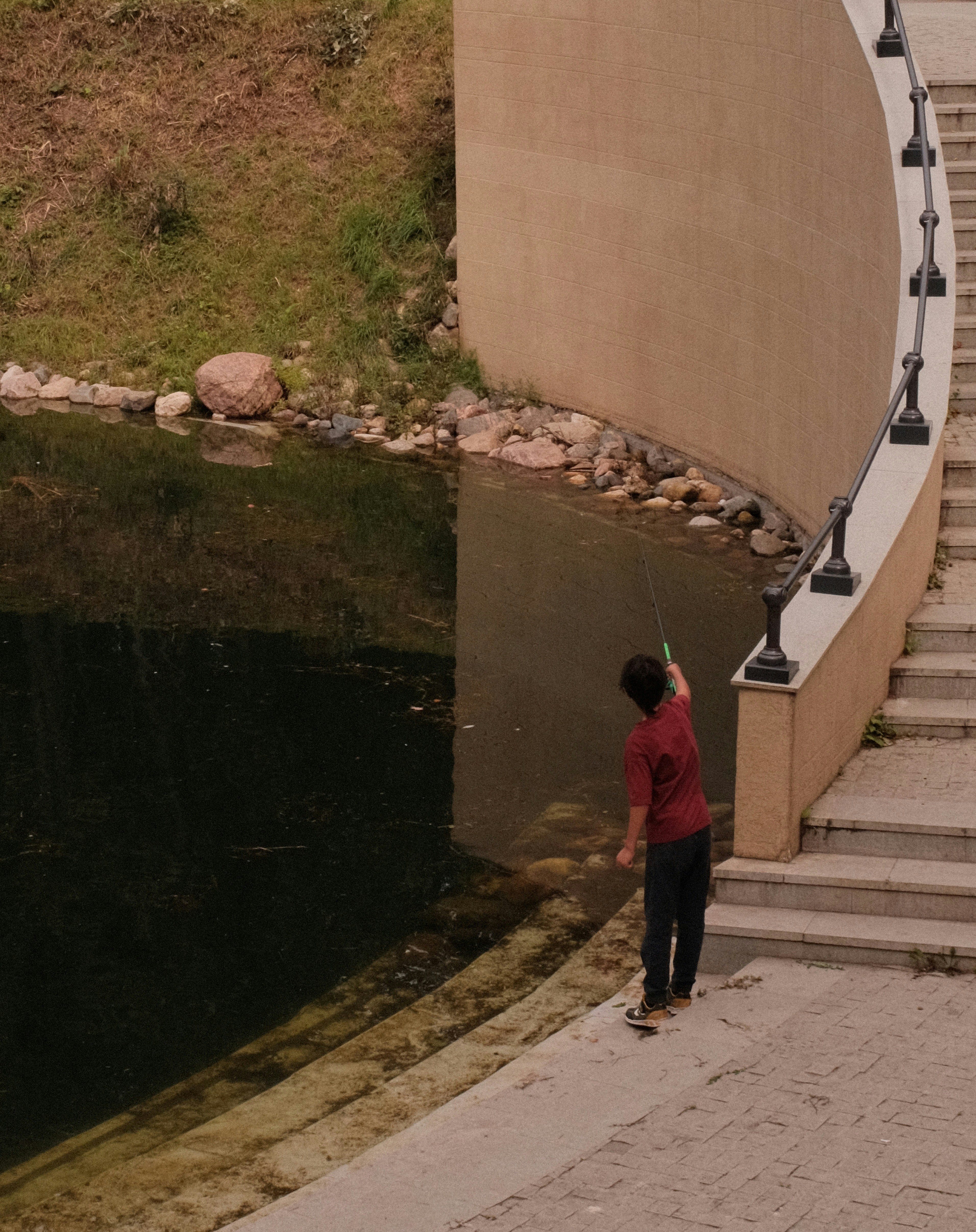 Young person fishing by a pond with stone stairs